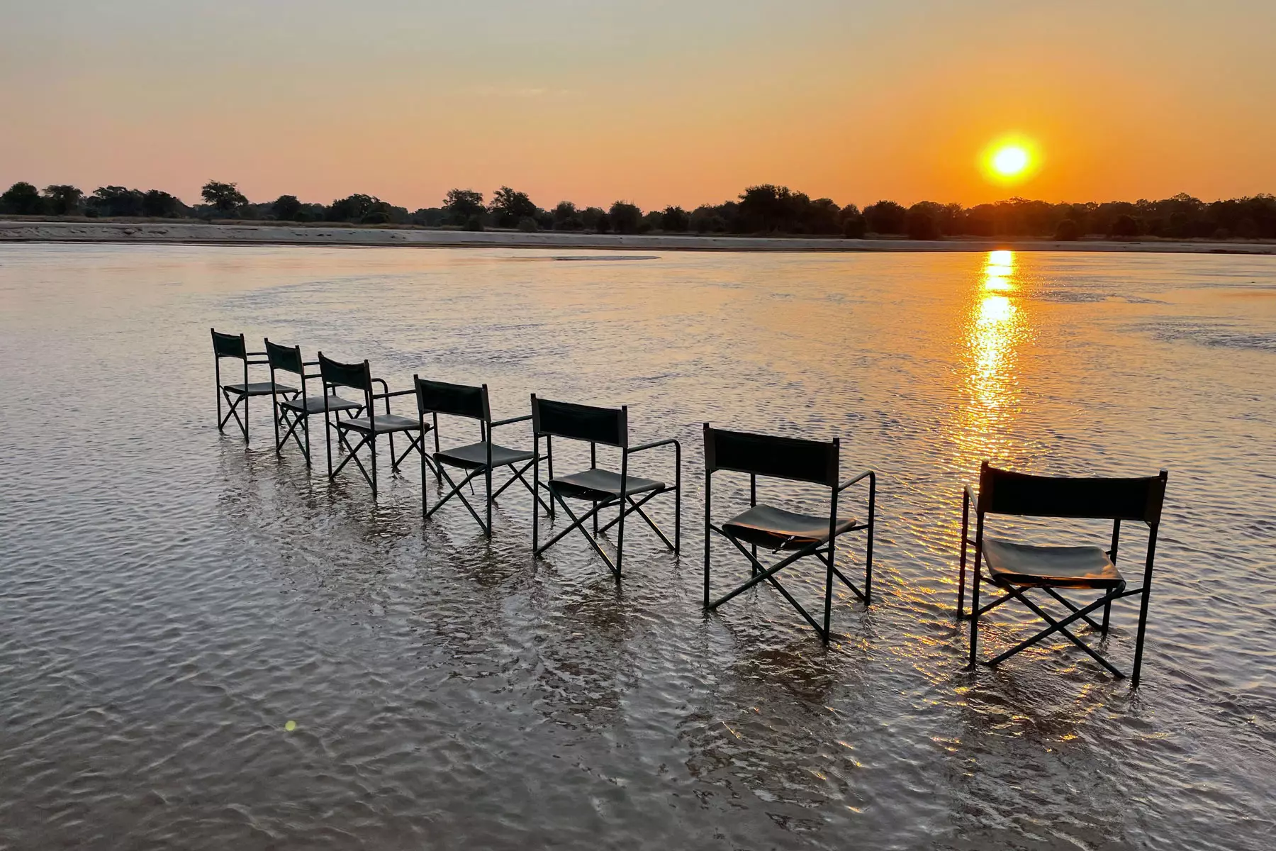 Plusieurs chaises assises dans une rivière peu profonde surplombant le coucher du soleil en Zambie