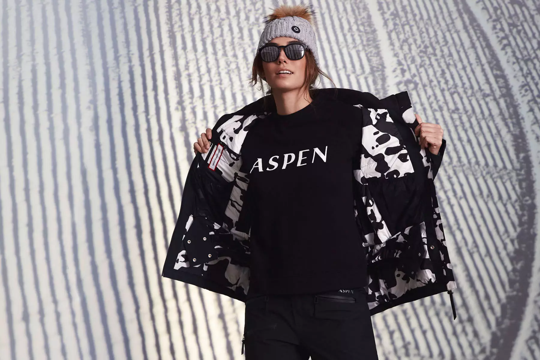 ASPENX स्की जैकेट और पोम्पोम टोपी पहने एक महिला