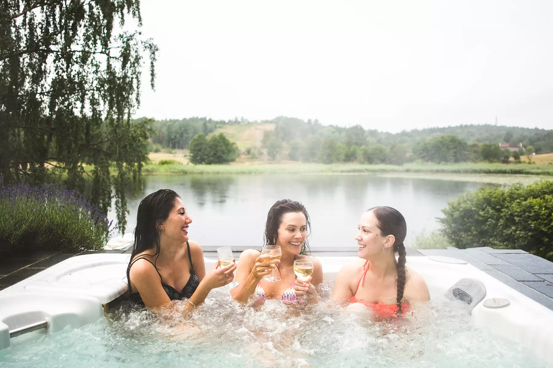 barátok élvezik a bort a pezsgőfürdőben a tóval szemben hétvégi kiruccanás közben