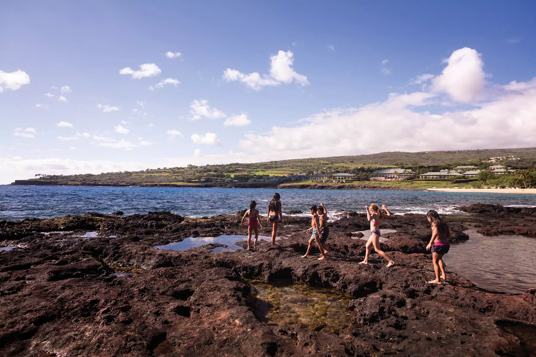 Bērni spēlējas uz akmeņiem pie okeāna viesnīcā Four Seasons Lanai