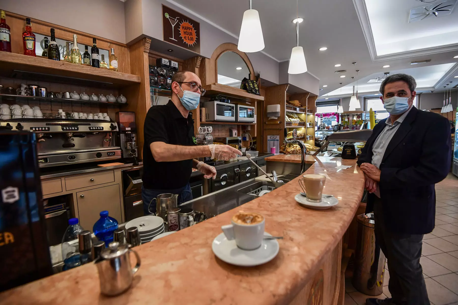 barista klientui, dėvinčiam veido kaukę, patiekia kapučino