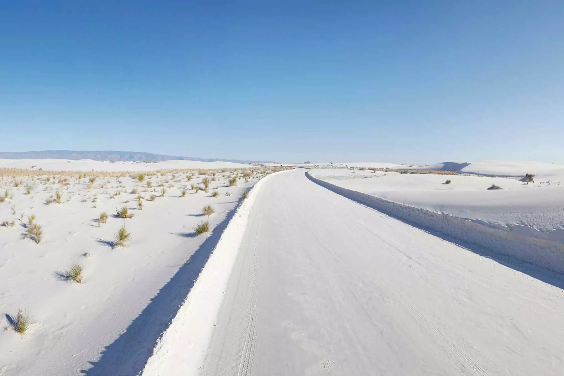 Prázdna cesta s bielym pieskom za slnečného dňa v národnom parku White Sands, Nové Mexiko, USA.