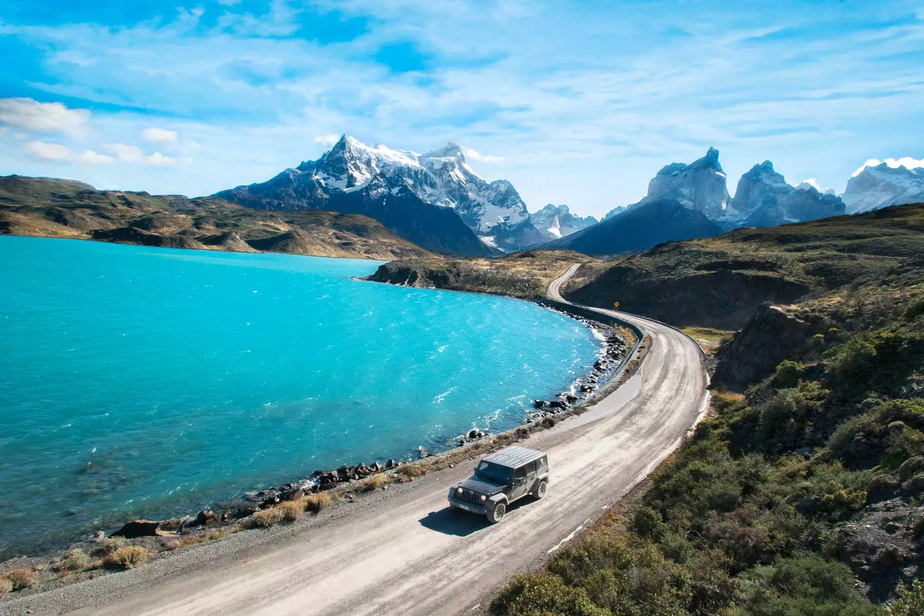 Yon djip pase bò dlo ble klè sou yon wout mòn nan Patagonia, Chili