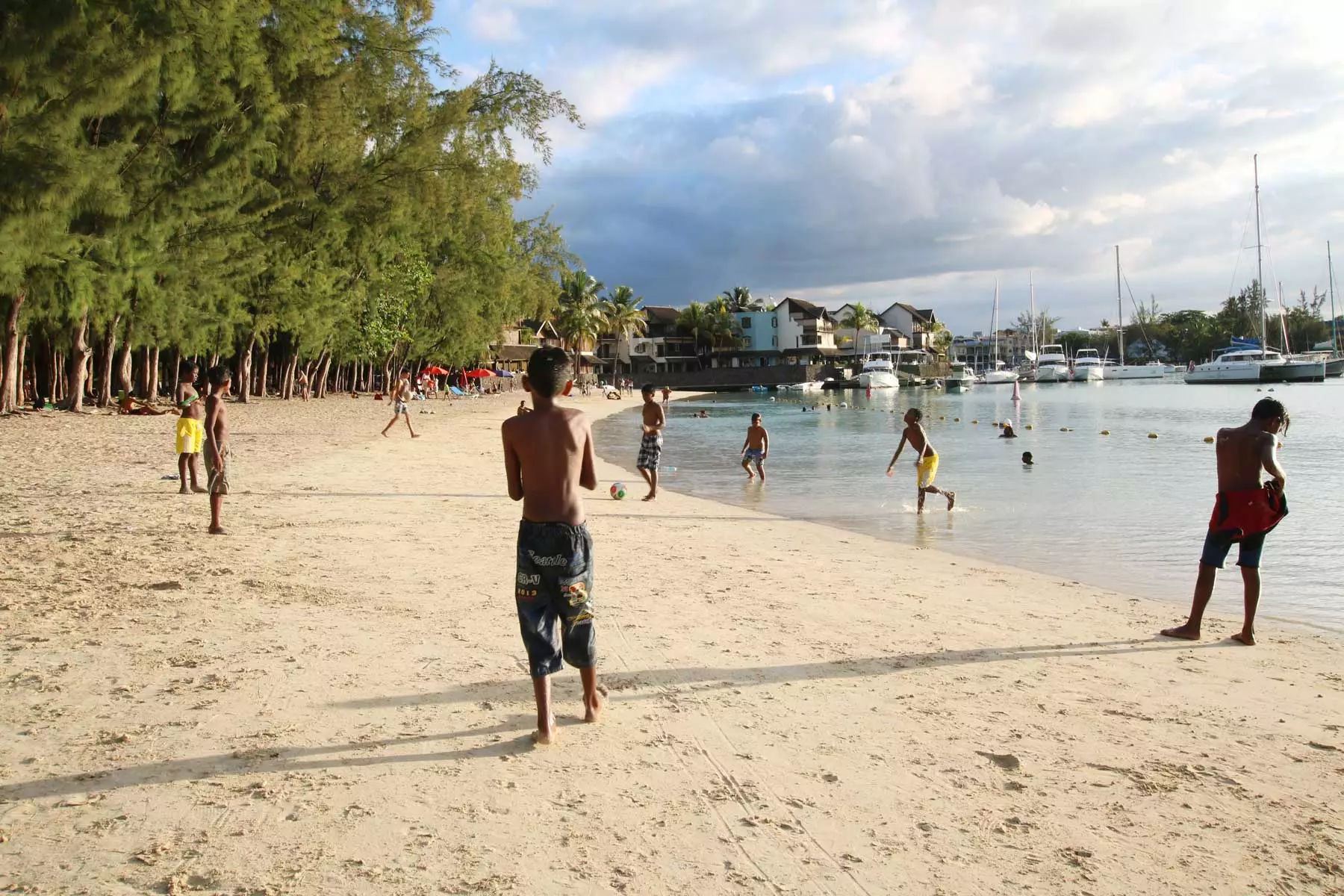 Chlapci hrajú futbal na pláži Grand Baie, Sunset, Maurícius