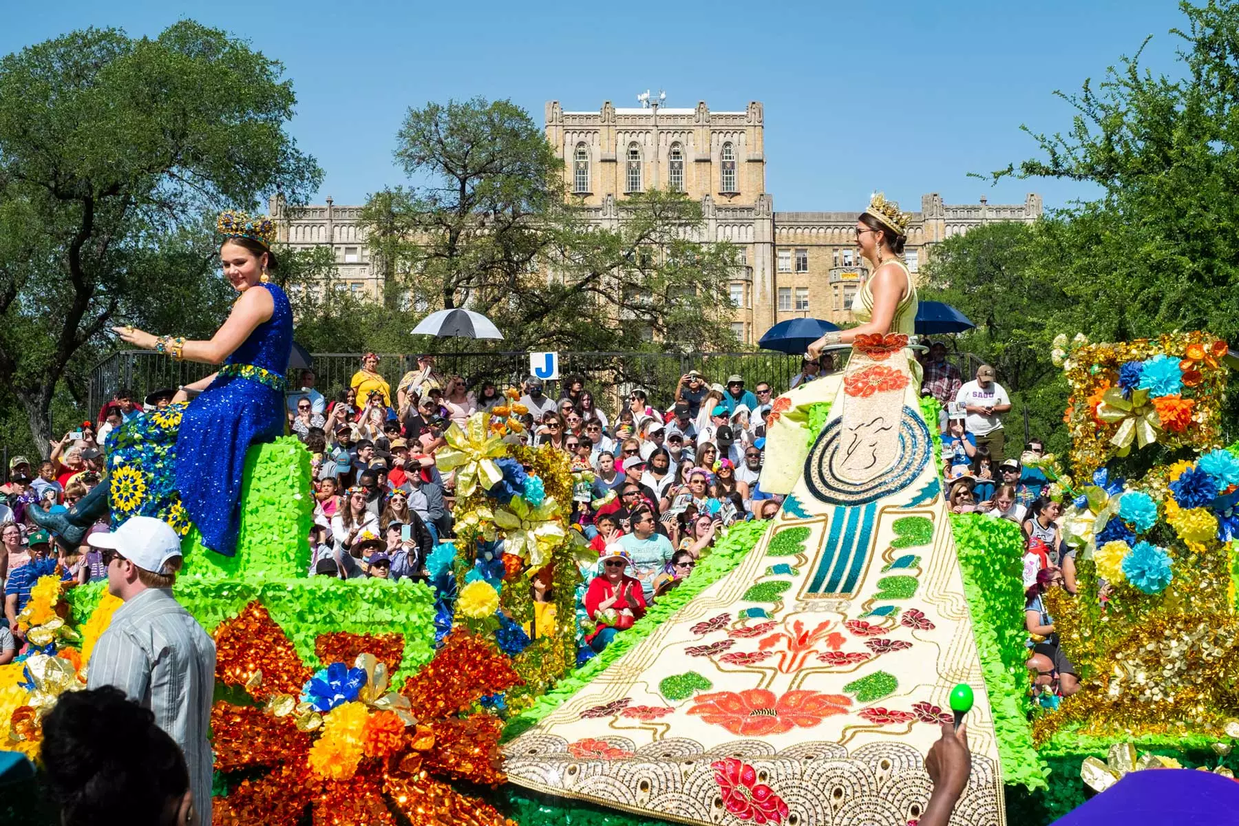 Dos duquesas se sientan en un puesto en un desfile de carrozas mientras atraviesan grandes multitudes.