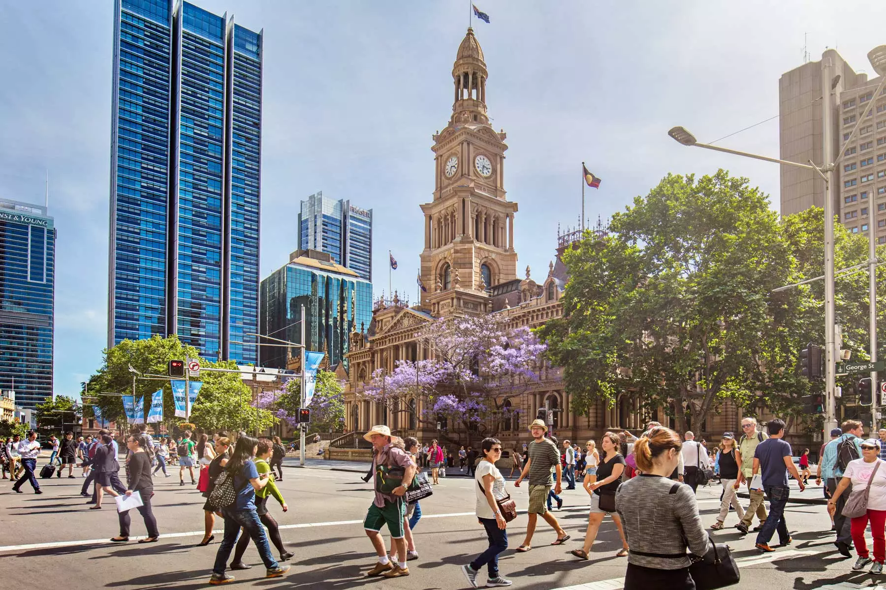 Orang-orang berjalan di sepanjang George Street di Sydney, Australia, dengan Sydney Town Hall di latar belakang