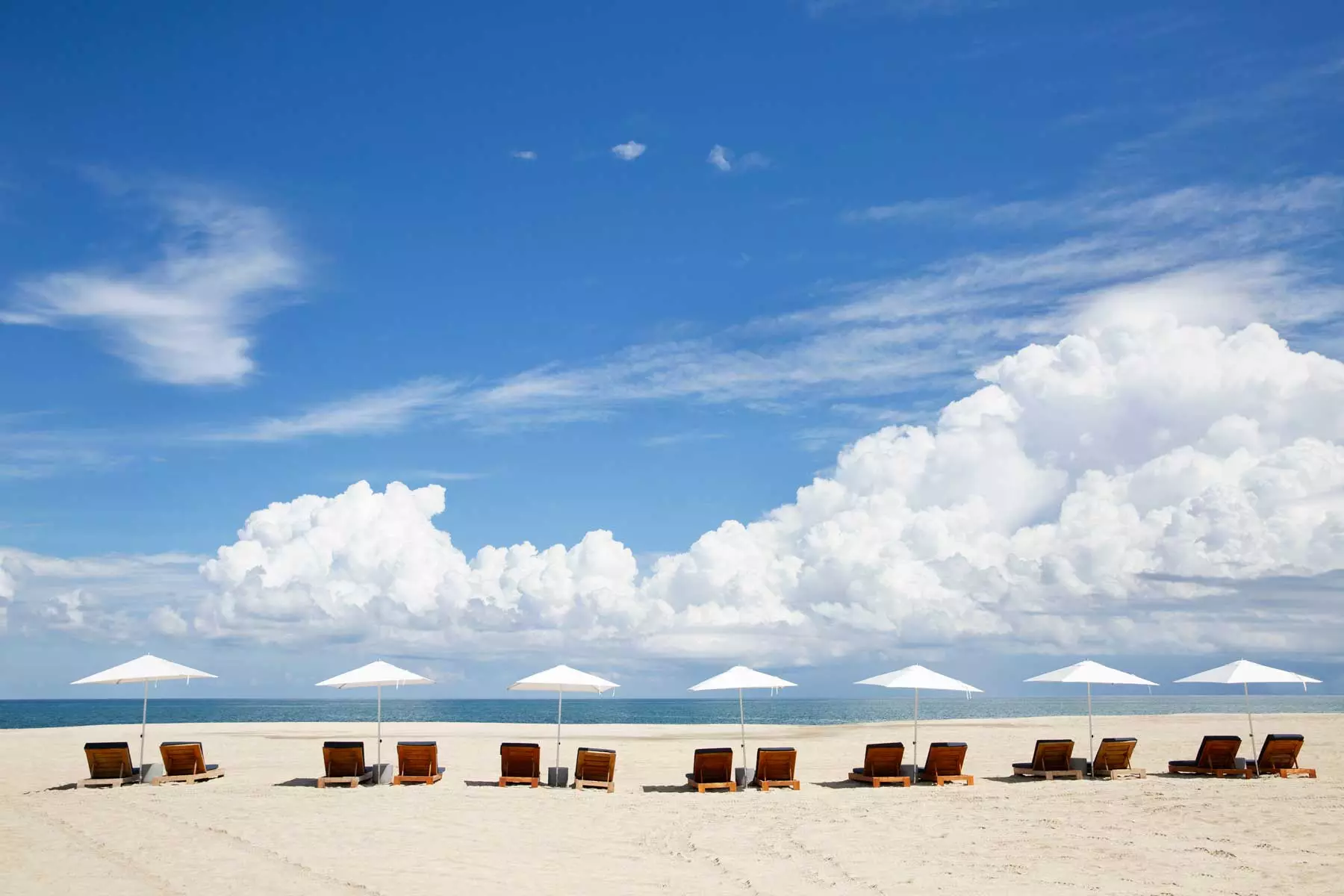 Strandstoele en sambrele by die Four Seasons Resort in Los Cabos, met blou lug en donserige wit wolke in die agtergrond