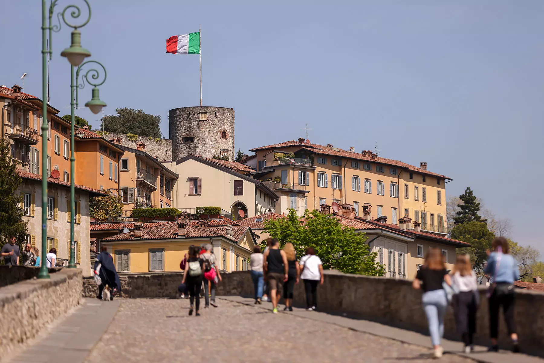 سائحون يمشون عبر جسر أعلى التل إلى البلدة القديمة (سيتا ألتا) في إيطاليا ، بيرغامو