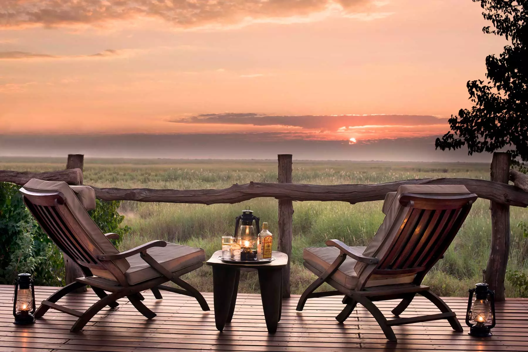 Twee ligstoelen op een houten terras kijkend naar de zonsondergang in Botswana