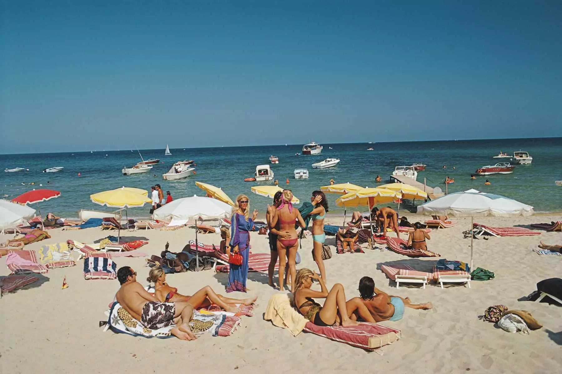 Folla ta’ nies li jżuru l-baħar chic fuq bajja f’San Tropez, fotografati minn Slim Aarons madwar l-1971