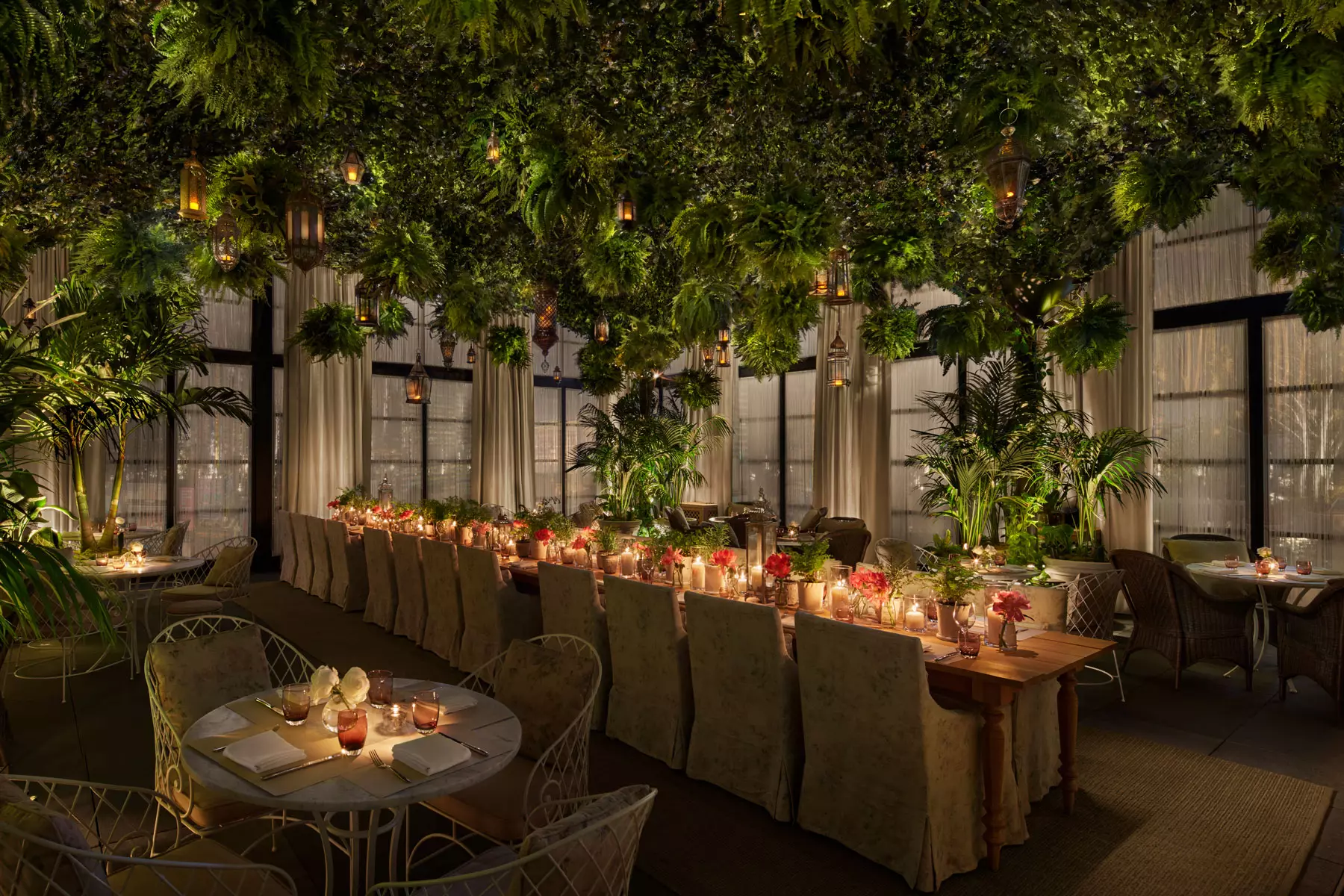 Un comedor con poca luz y plantas verdes que cuelgan del techo en el jardín de The Times Square EDITION