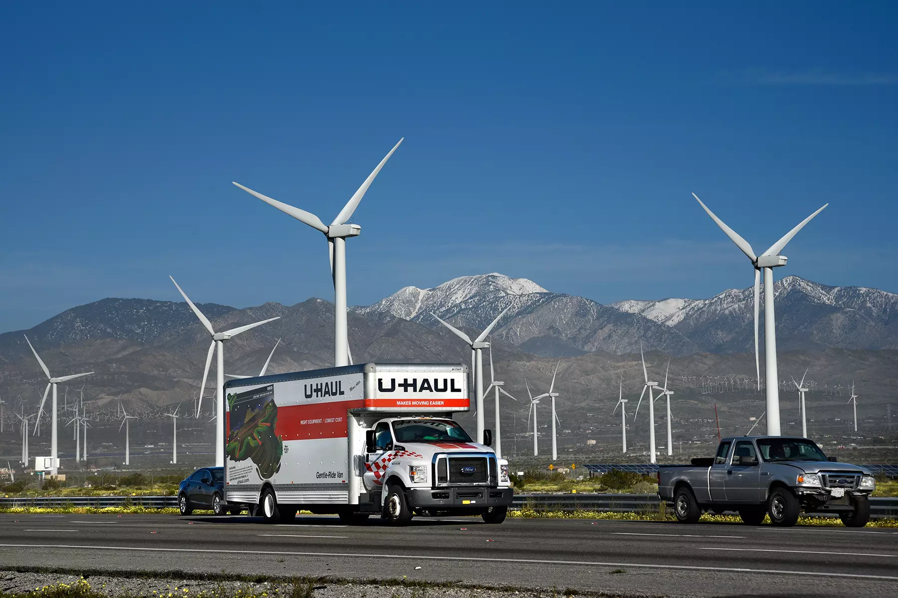 Ciężarówka U-Haul i inne pojazdy poruszają się wzdłuż autostrady międzystanowej 10 i farmy wiatrowej San Gorgonio Pass w pobliżu Palm Springs w Kalifornii.