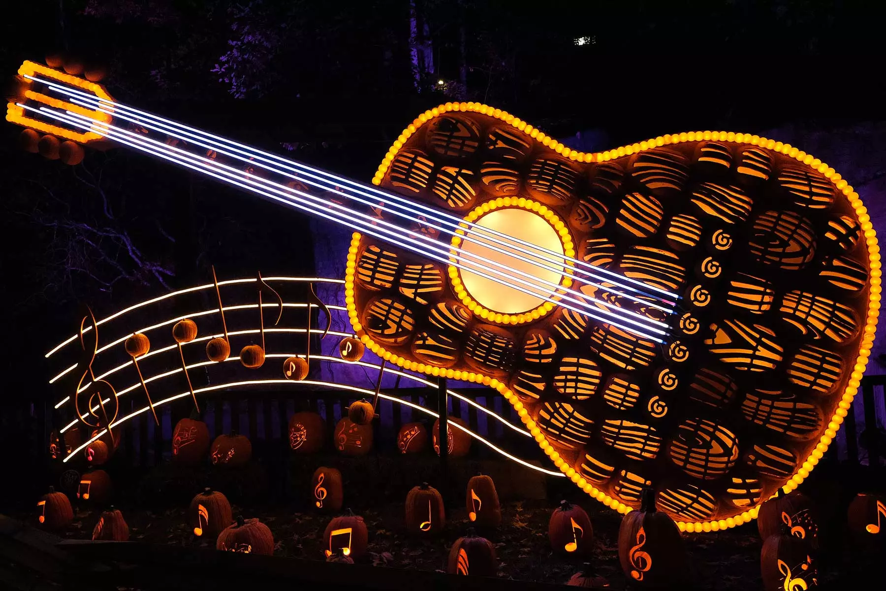 Een oversized sculptuur van een gitaar gebouwd van uitgehouwen pompoenen die 's nachts gloeien