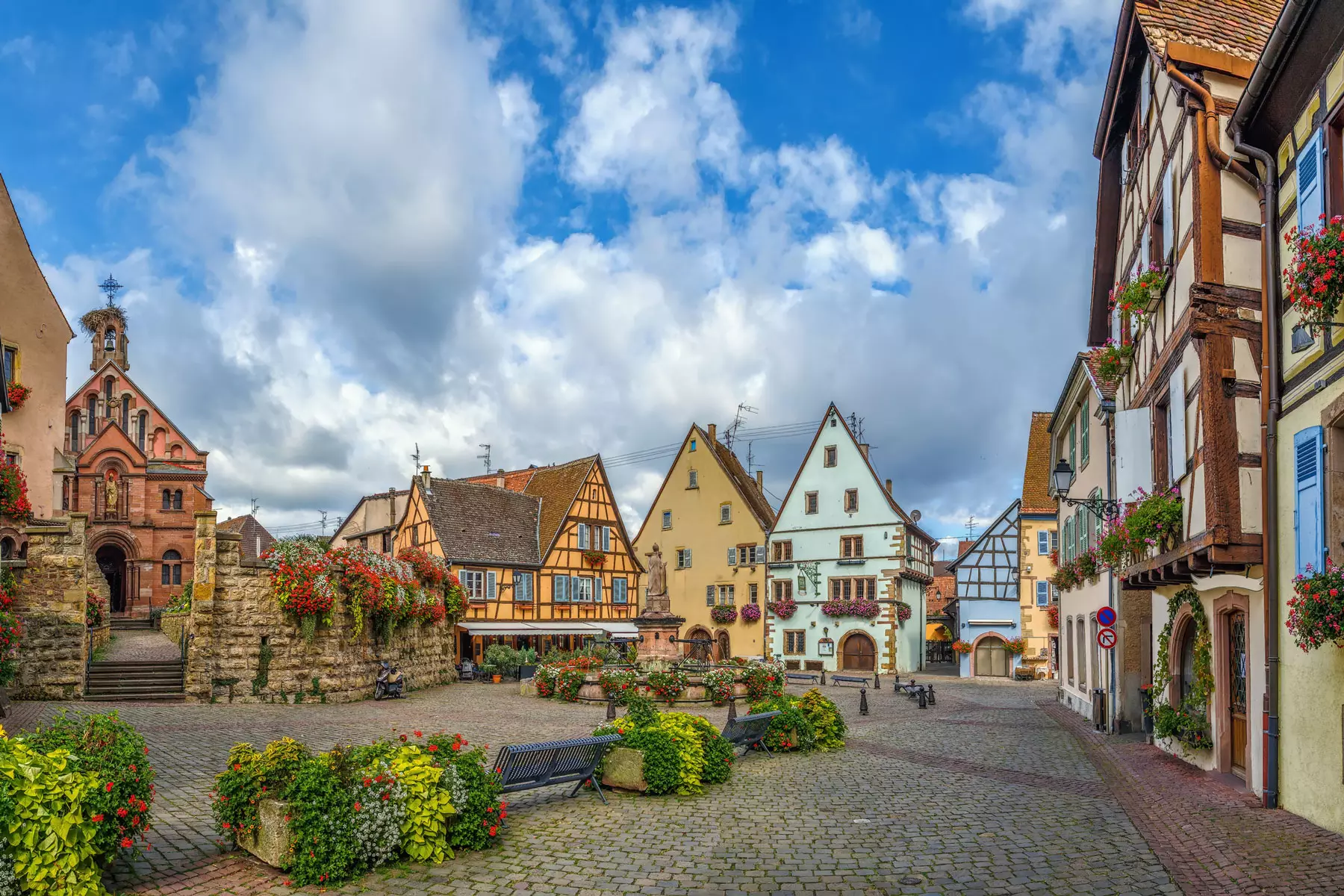 በEguisheim፣ Alsace፣ ፈረንሳይ ውስጥ ከሊቀ ጳጳስ ሊዮ IX ሐውልት ጋር ዋና አደባባይ ከቤተክርስቲያን እና ምንጭ ጋር