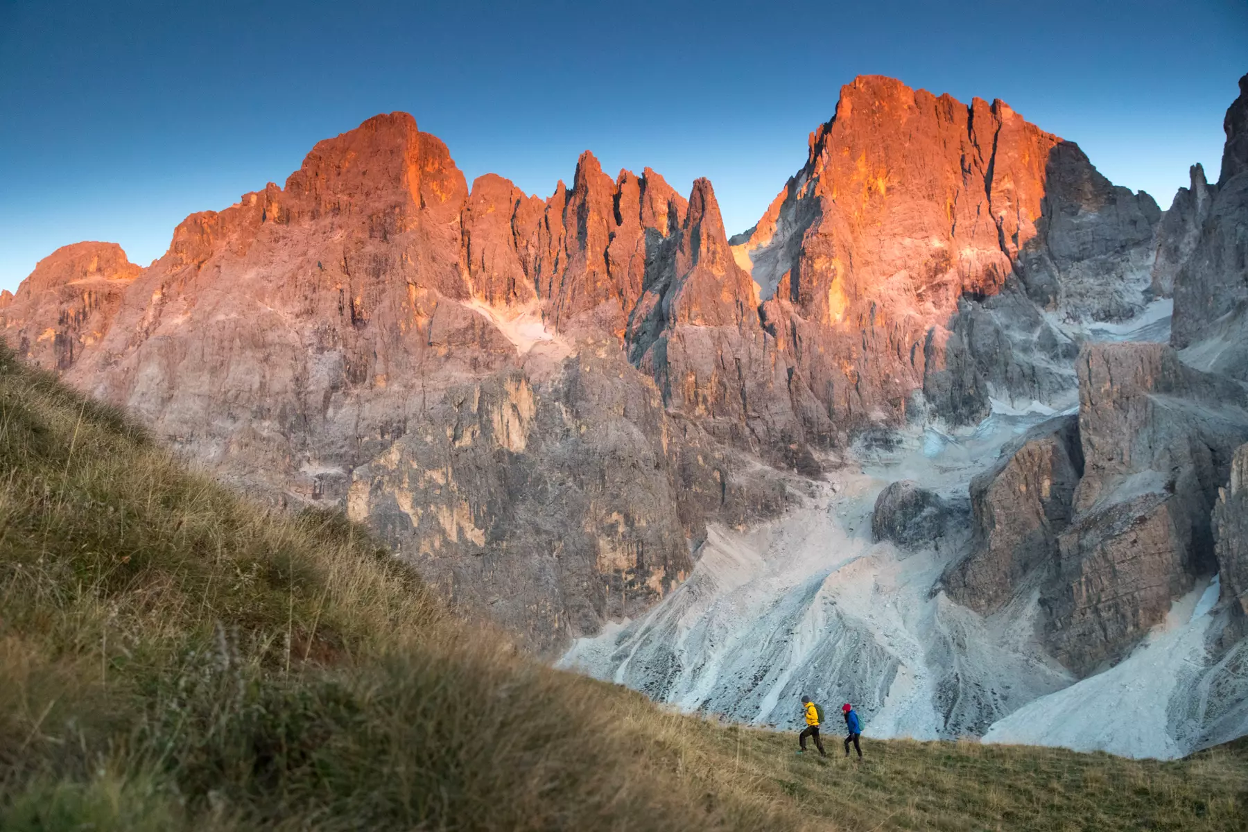 Dos personas caminando en Trentino con montañas rústicas gigantes