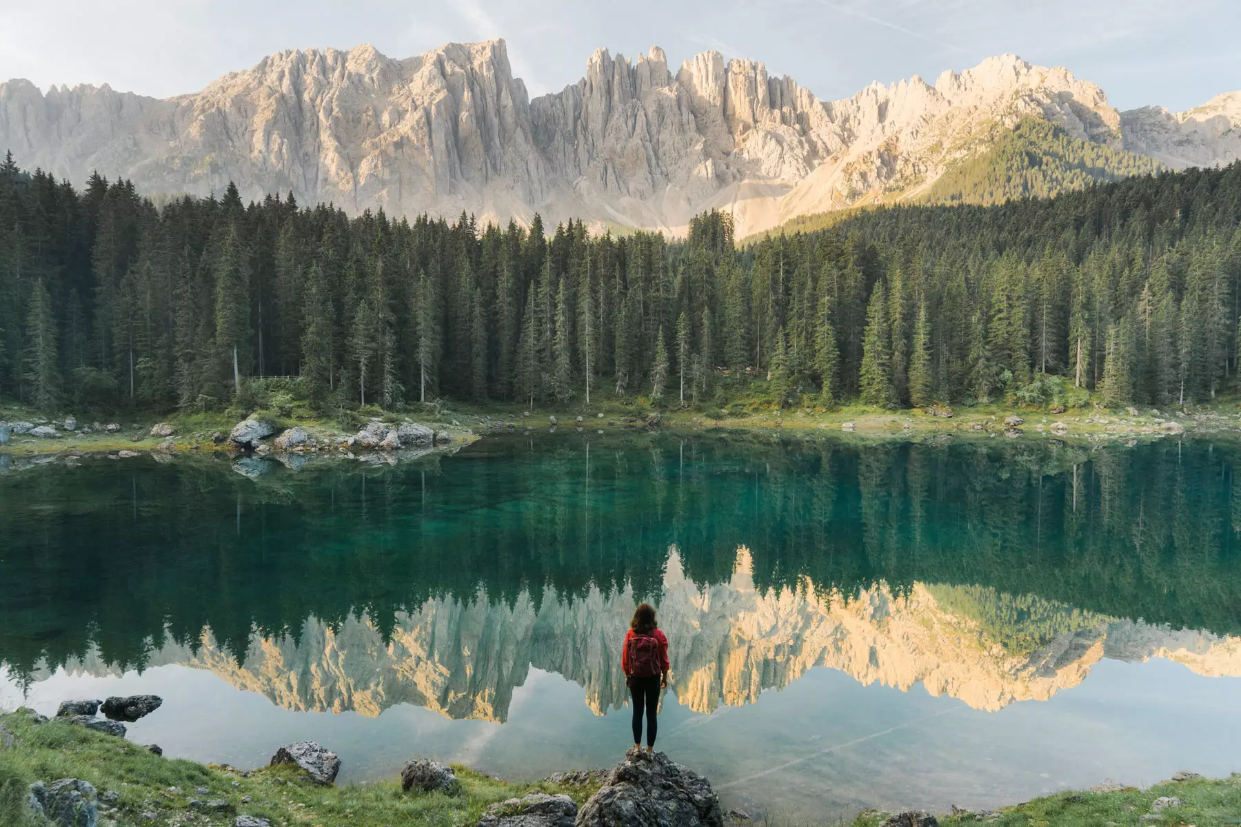 Mujer de pie cerca del lago que refleja los Dolomitas en Italia