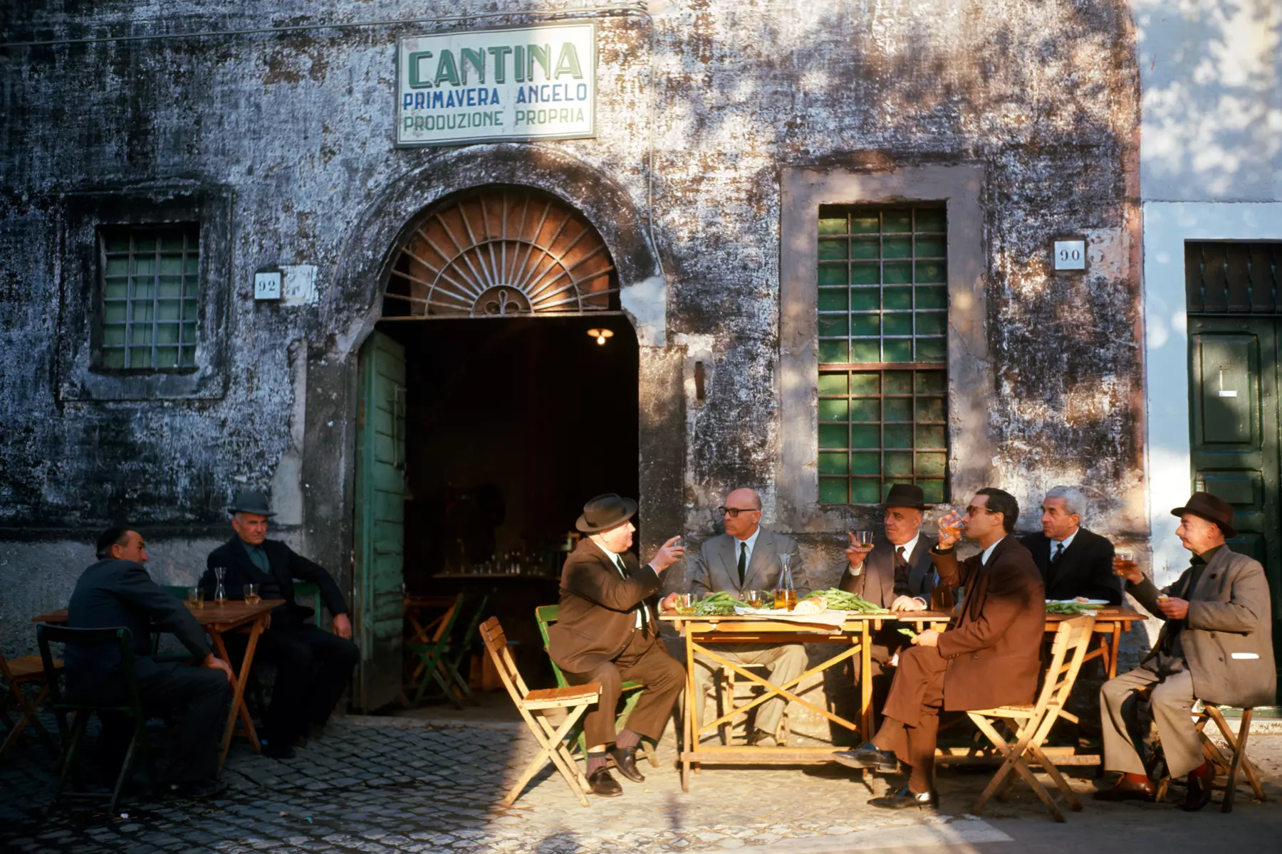 Të moshuar të ulur në tavolina jashtë një taverne në Itali