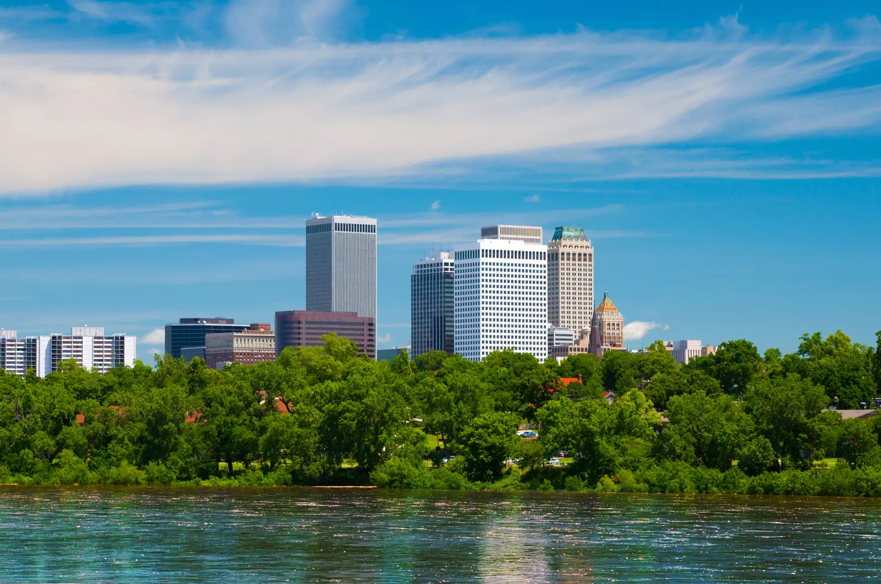 Tulsa centrums skyline med træer og Arkansas-floden i forgrunden.