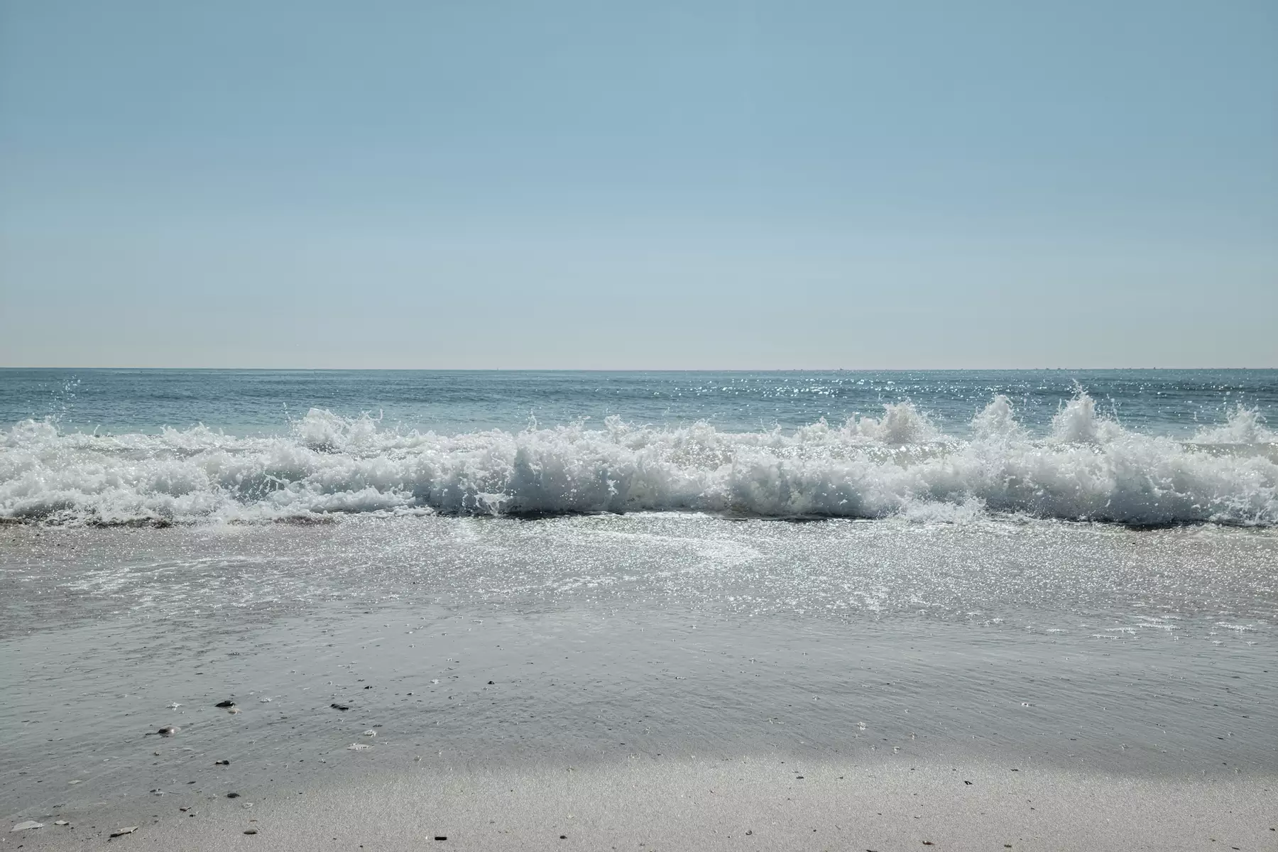 Spiaggia Rockaway, oceano tranquillo e vuoto con un bagliore pacifico sullo sfondo.