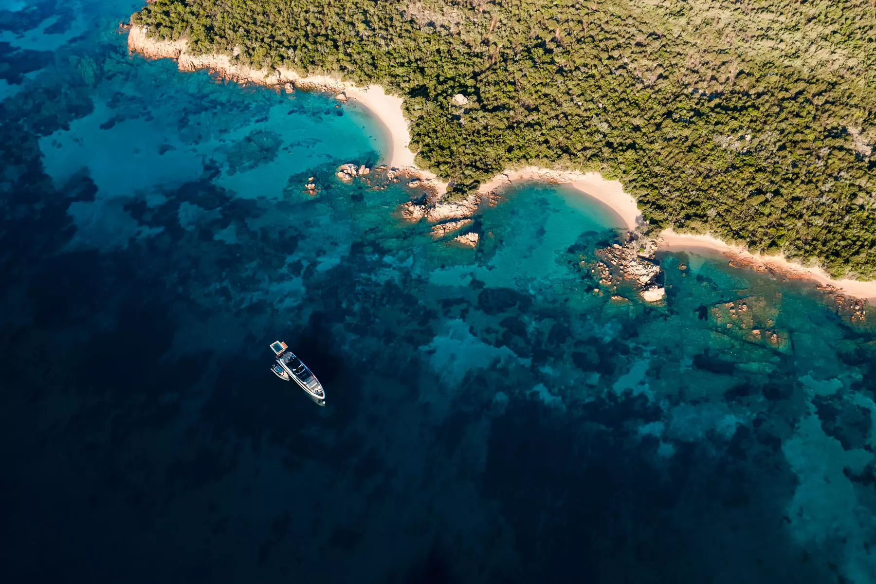 Pemandangan dari atas, pemandangan udara yang menakjubkan dari garis pantai hijau dengan beberapa pantai yang indah dan kapal pesiar yang berlayar di atas air pirus. Liscia Ruja, Costa Smeralda, Sardinia, Italia.