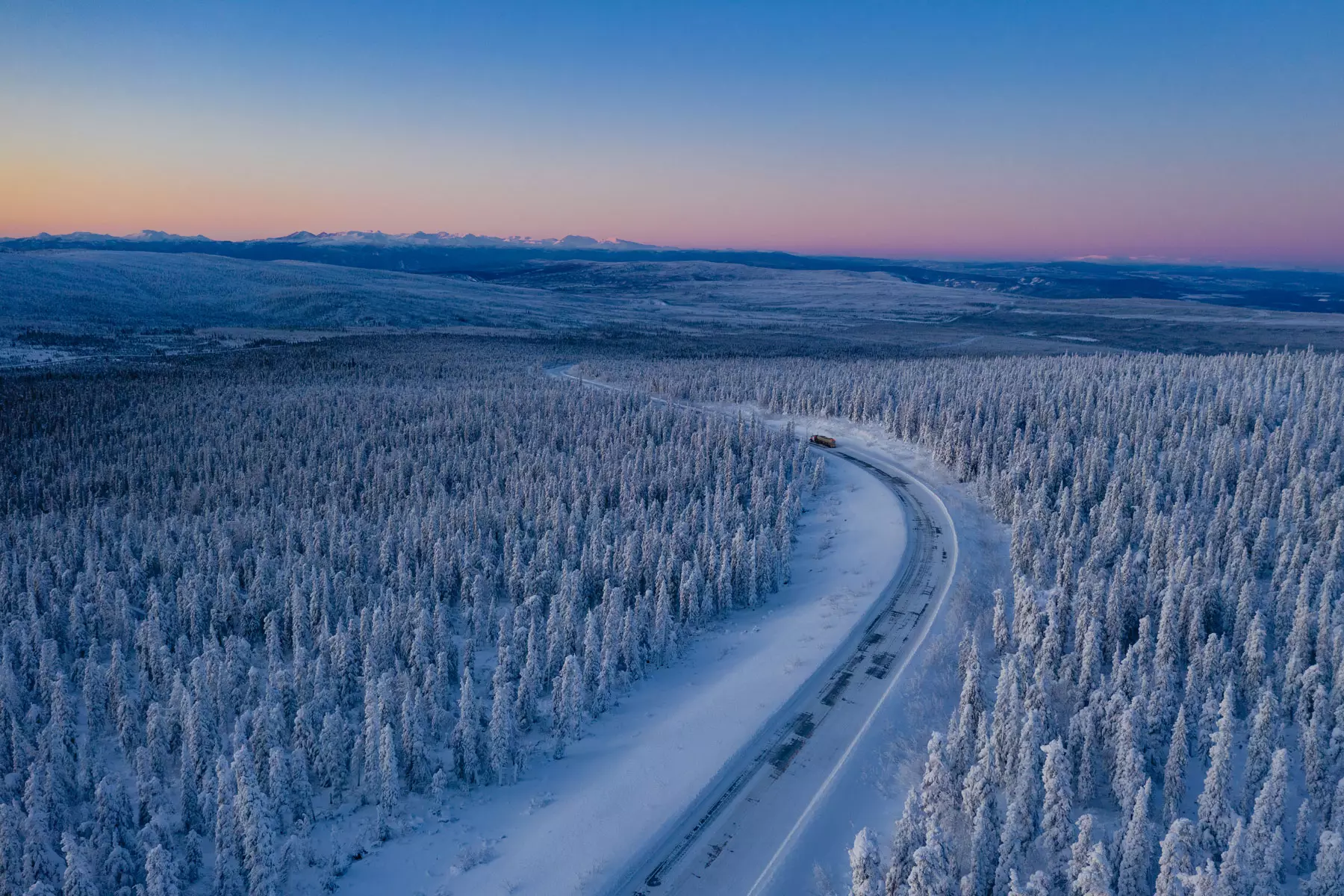 Luftfoto ved solnedgang af et stort vinterlandskab af fyrretræer dækket af sne ud for Dalton Highway i Alaska