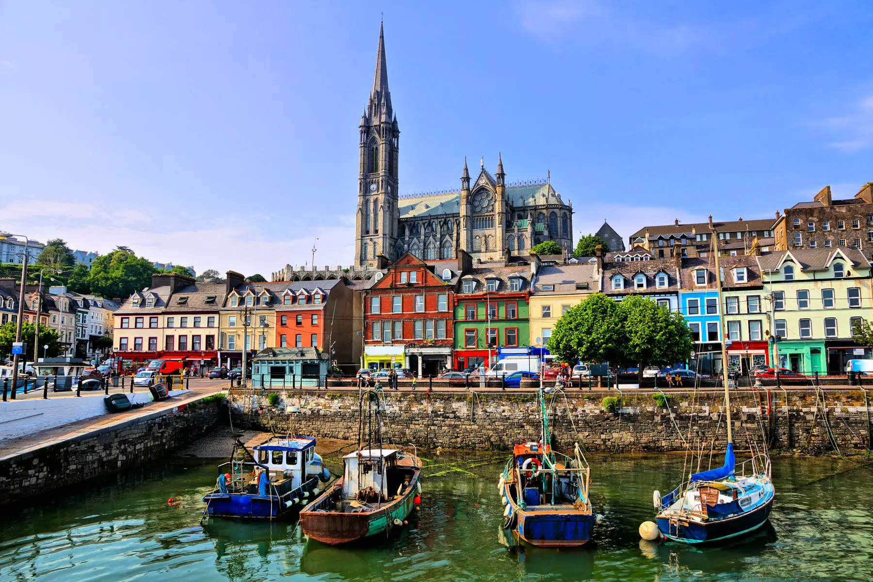 අයර්ලන්තයේ Cobh, County Cork වරායේ පසුබිමේ ආසන දෙව්මැදුර සහිත වර්ණවත් ගොඩනැගිලි සහ පැරණි බෝට්ටු