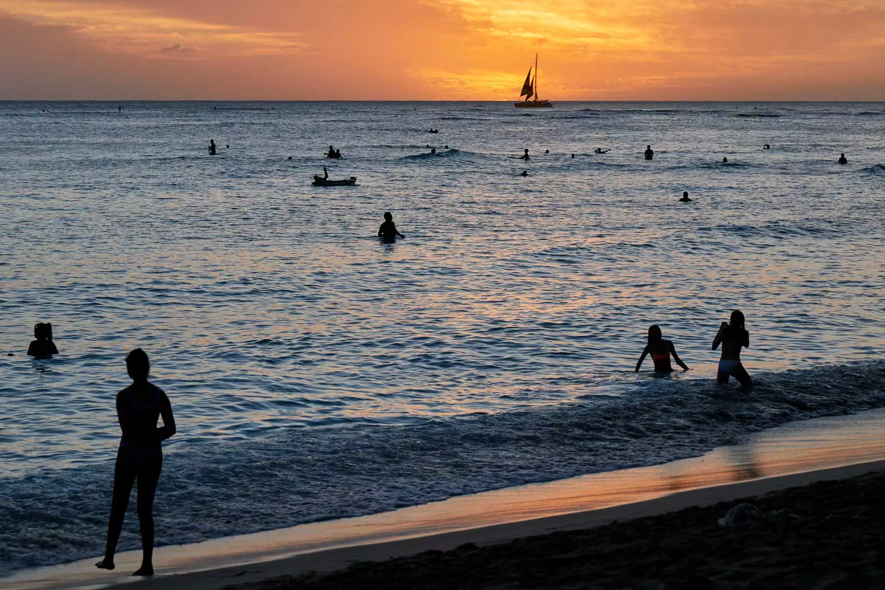 Menschen im Wasser am Strand von Waikiki, Hawaii, bei Sonnenuntergang