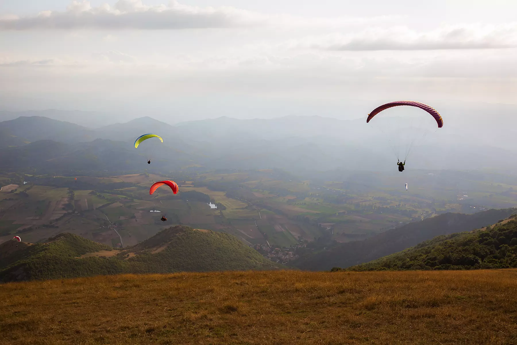 Paraglisaviadiloj flugantaj super monta pejzaĝo en Umbrio