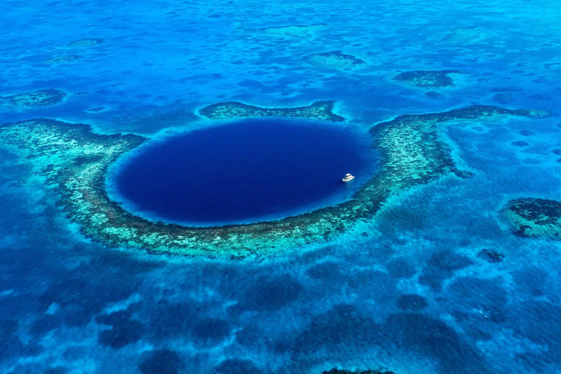 Belize ကမ်းလွန်ရှိ Great Blue Hole တွင် ရပ်နားထားသော သင်္ဘောတစ်စင်း၏ ဝေဟင်မြင်ကွင်း