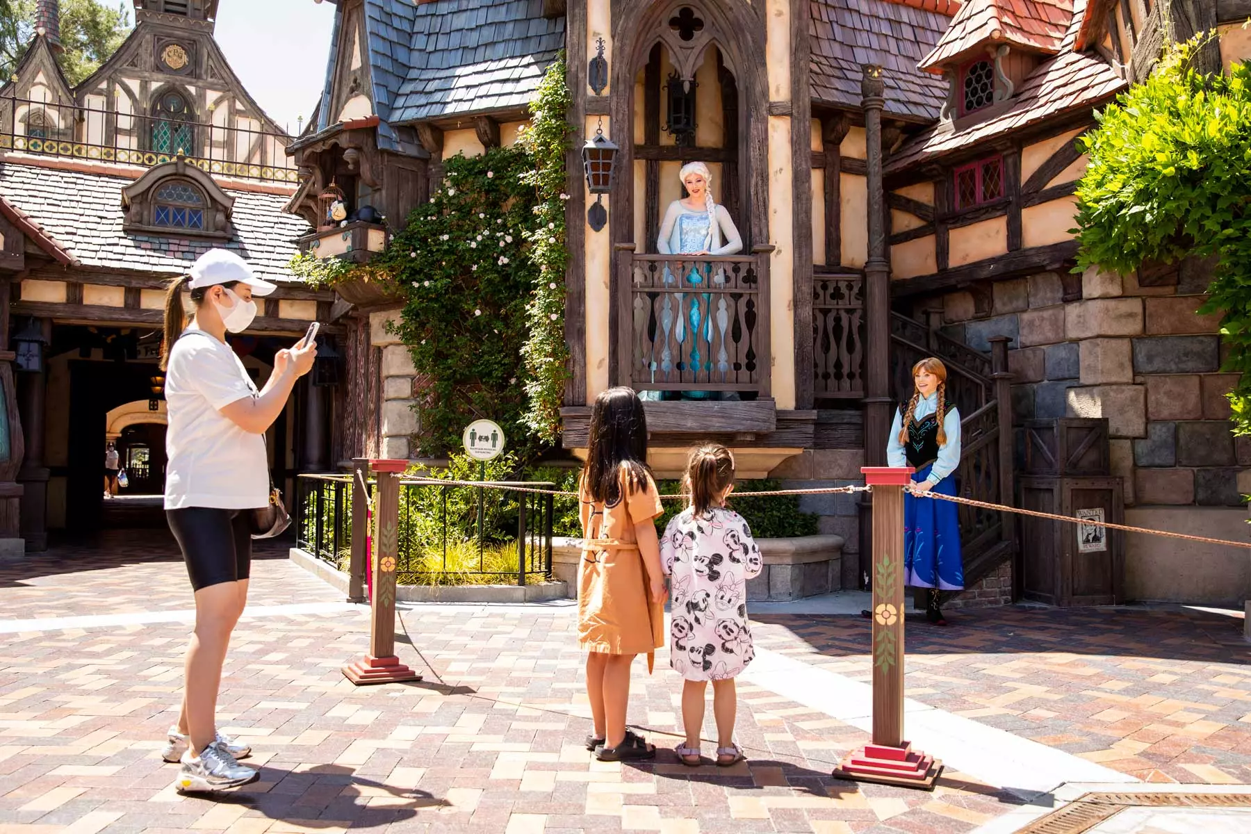 Una famiglia scatta foto e ha un'interazione socialmente distante con i personaggi di Elsa e Anna al Disneyland Resort di Anaheim, in California.