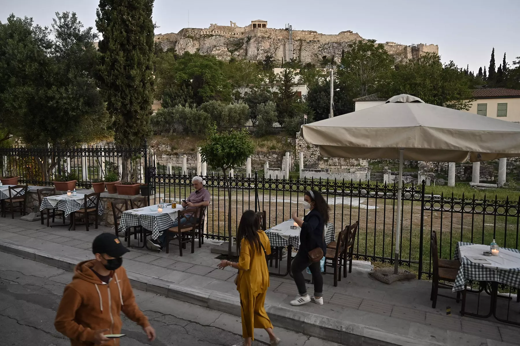 tūristi iet garām restorānam, no kura paveras skats uz Romas agoru un Akropoles kalnu Atēnās