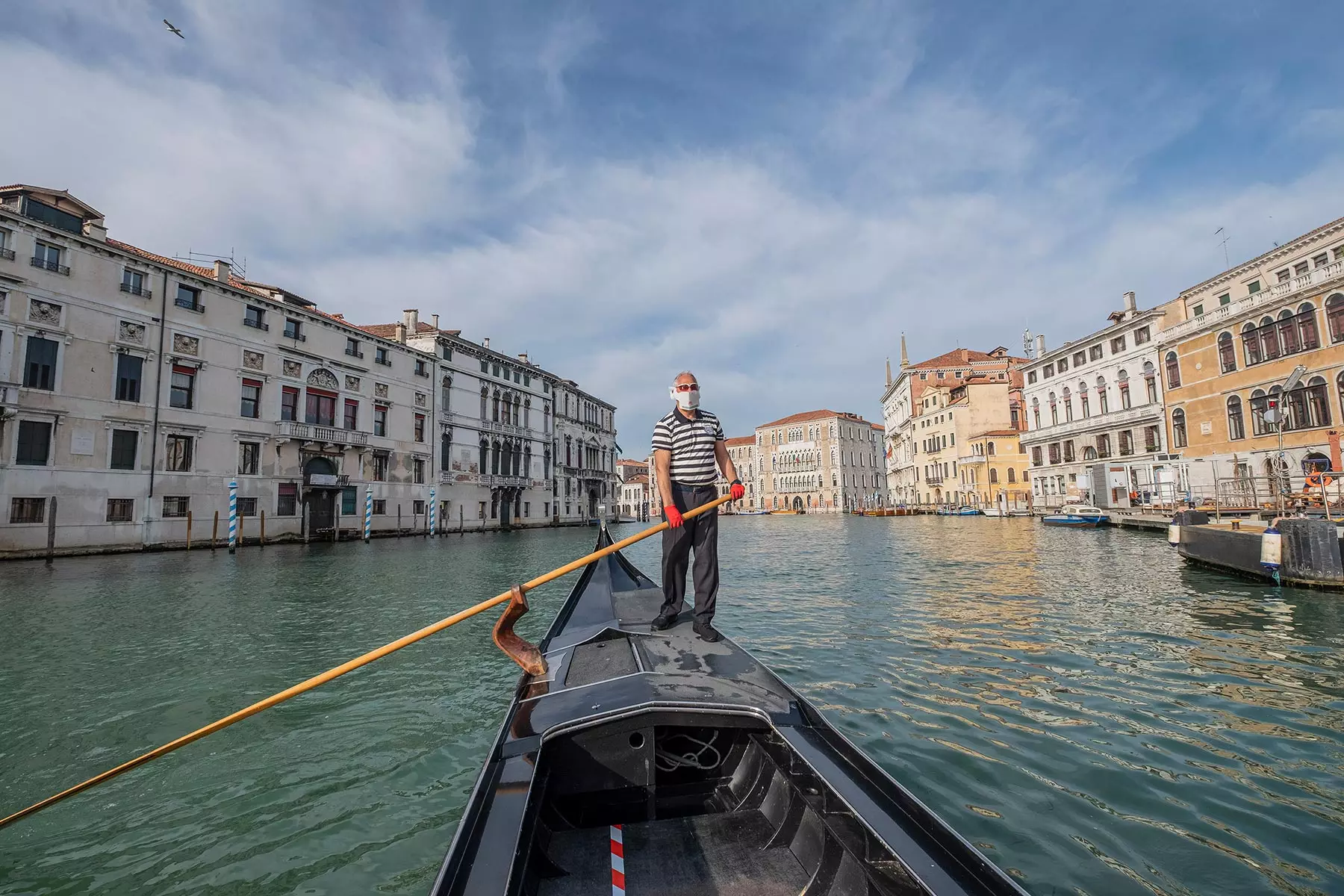 Gondolier a cikin abin rufe fuska da safar hannu a tashar Saint Tomà mara komai lokacin da sabis ya sake farawa a Venice, Italiya.