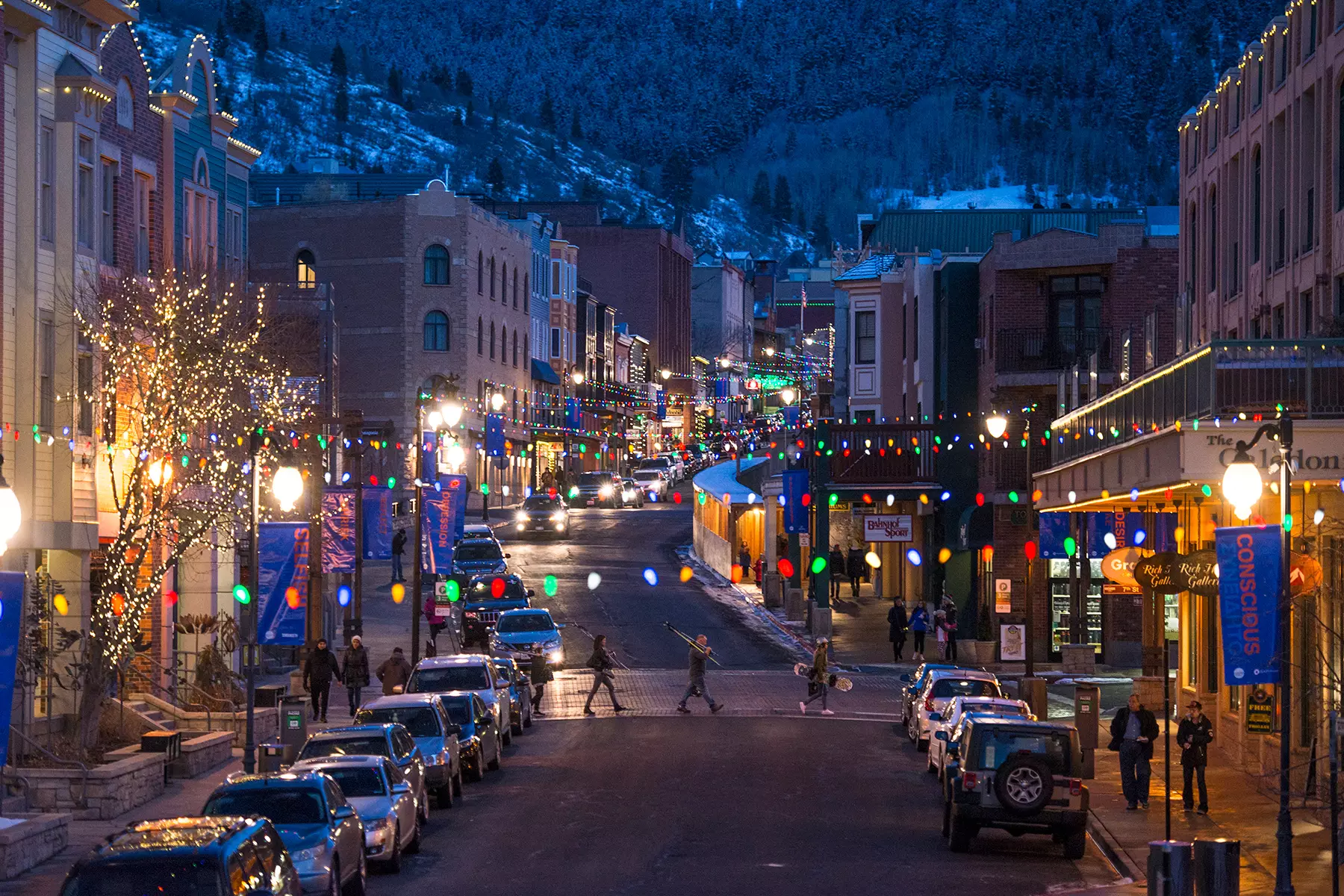 Yon fanmi pasyone ski ak planch nèj travèse yon Main Street Park City limen ak dekore fèt.