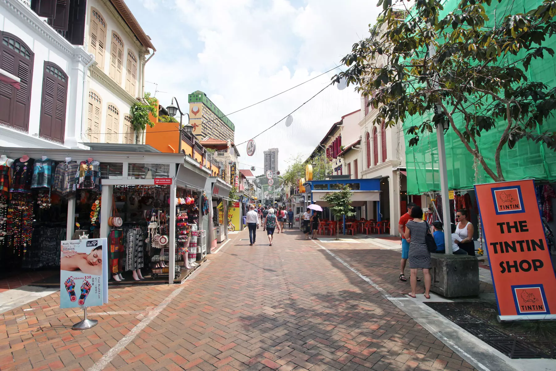 Kilátás a Pagoda utcára Szingapúr kínai negyedében, régi boltházakkal, ruhákat és ajándéktárgyakat árusító piaci standokkal, valamint számos gyalogossal, akik az utcán sétálnak.
