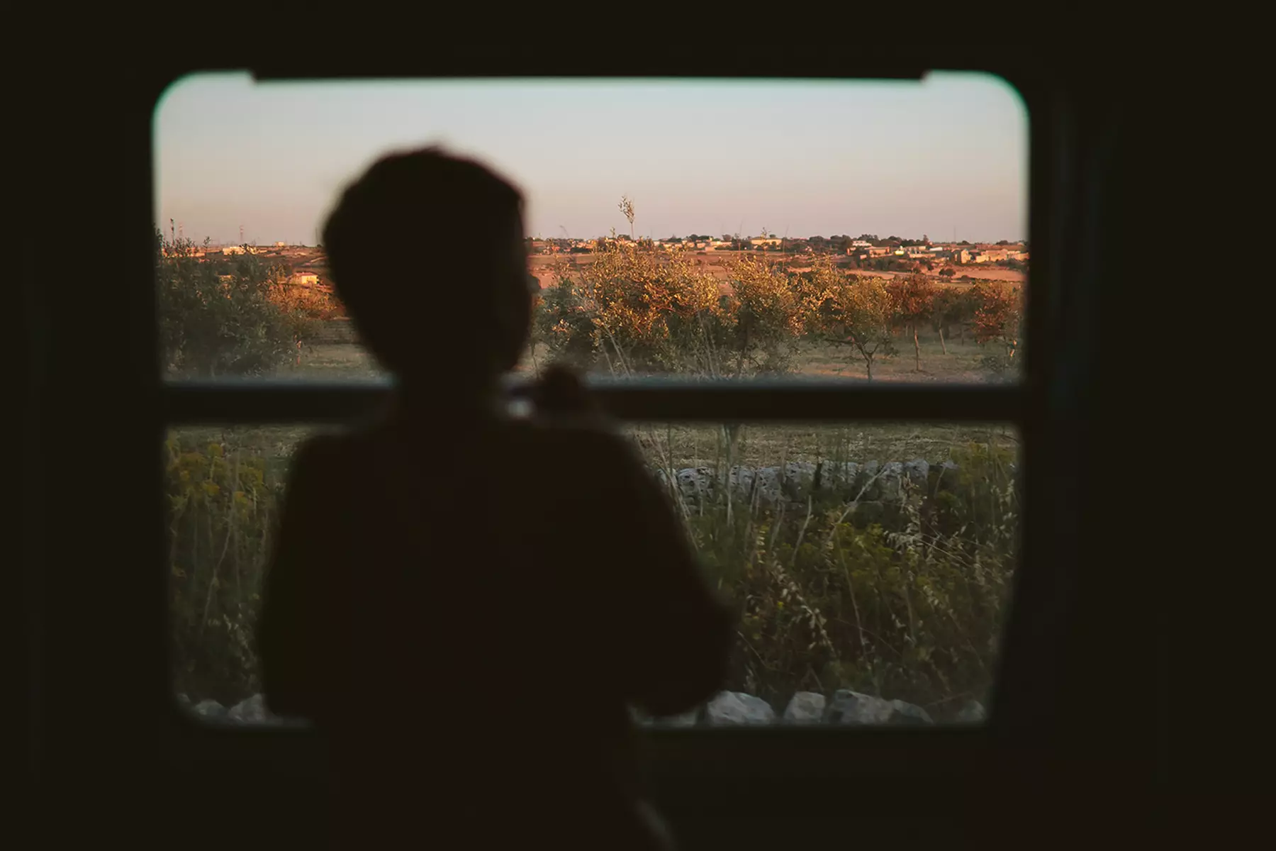 Silhoueta kurik li Sîcîlyayê di pencereya trênê de dinihêre