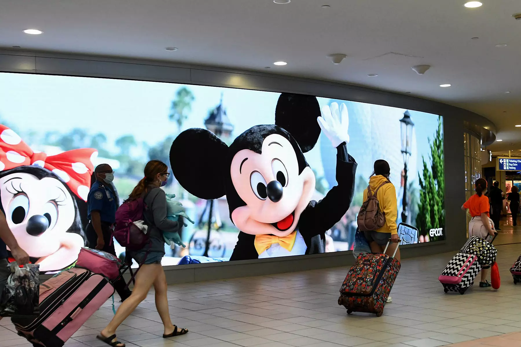 Orlando tarptautiniame oro uoste keliautojai eina pro iškabą, reklamuojančią Walt Disney World