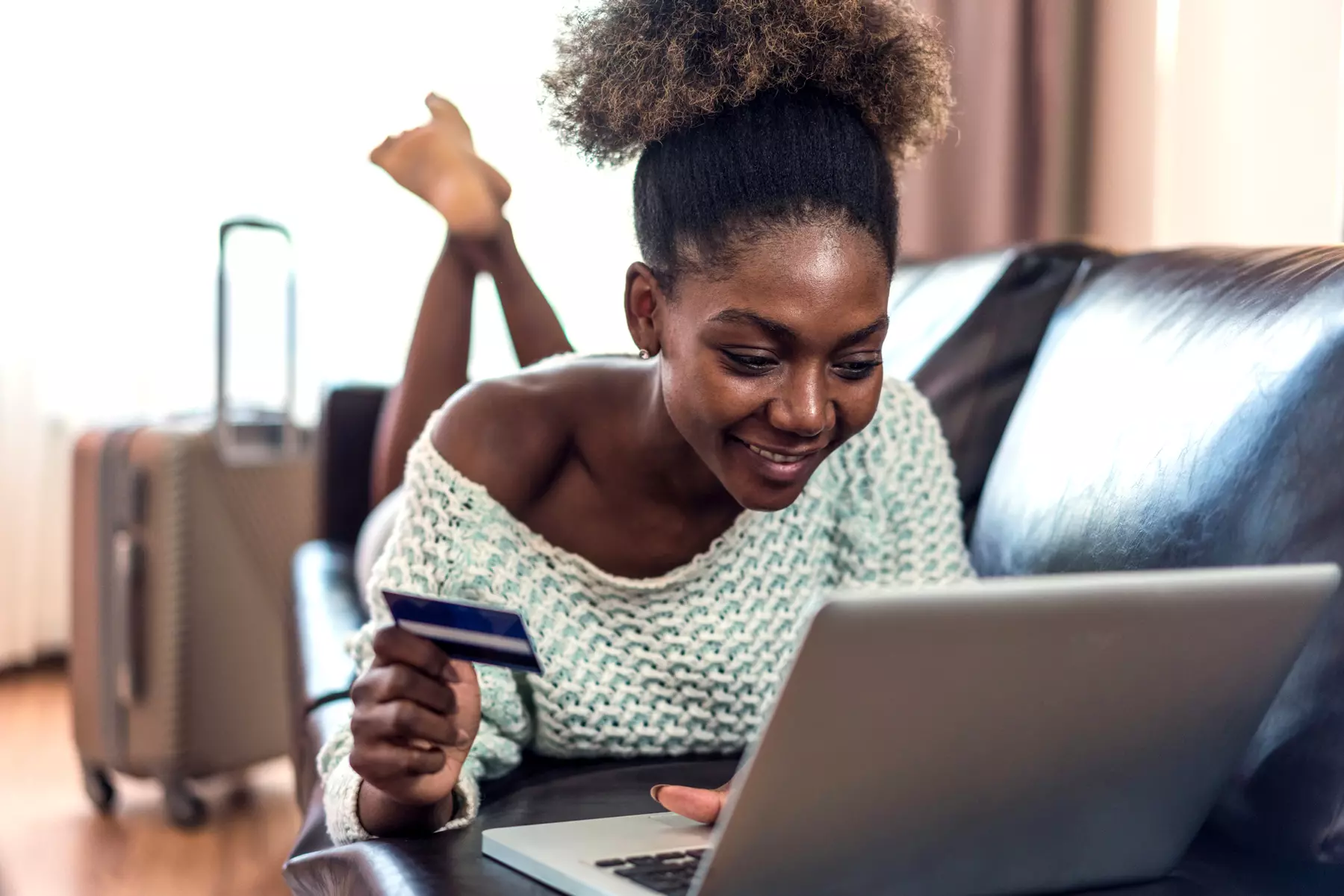 Genç Siyah kadın seyahate hazırlanıyor ve dizüstü bilgisayarında çevrimiçi ödeme yapıyor.