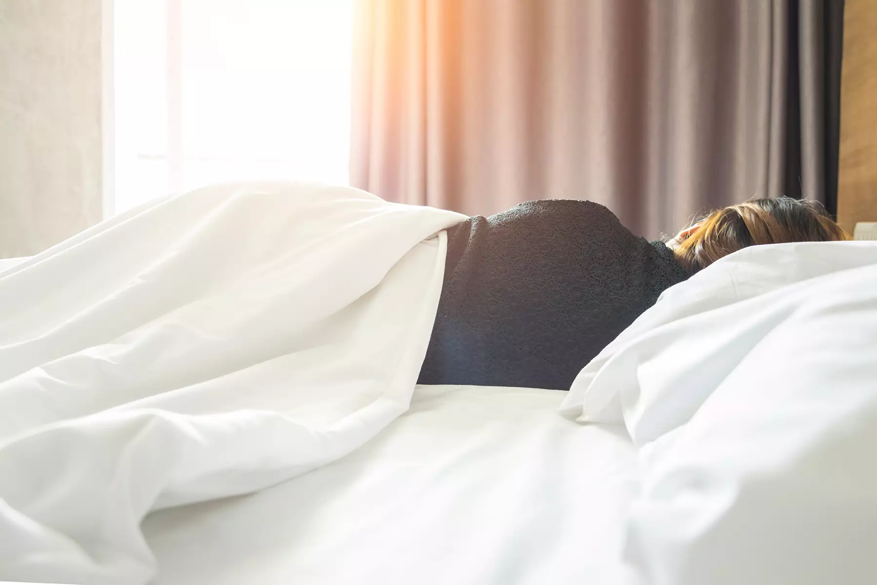 Sieviete guļ uz baltas gultas viesnīcas istabā