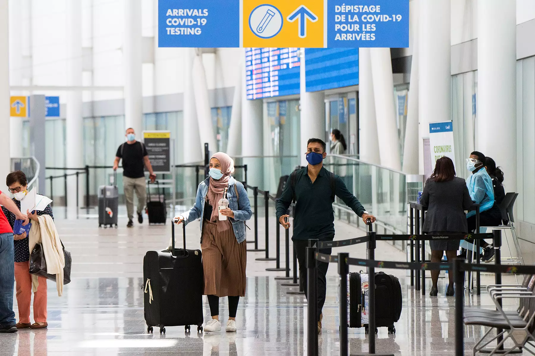 Патниците кои носат маски за лице излегуваат од салата за пристигнување на меѓународниот аеродром во Торонто Пирсон