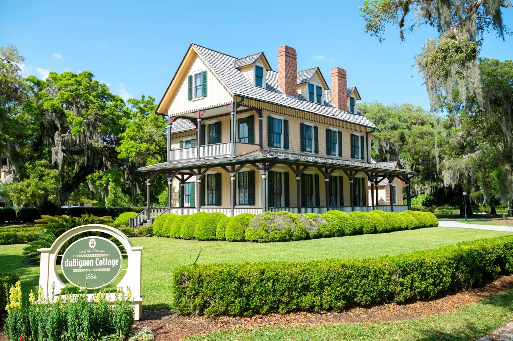 Herenhuis op Jekyll Island, heldere zonnige dag, blauwe lucht, volledig gebouw in shot, huis met struiken en gazon aan de voorkant en zijkant, bomen op de achtergrond, huis geschoten vanaf zijaanzicht met 3/4 voorkant en 1/4 kant