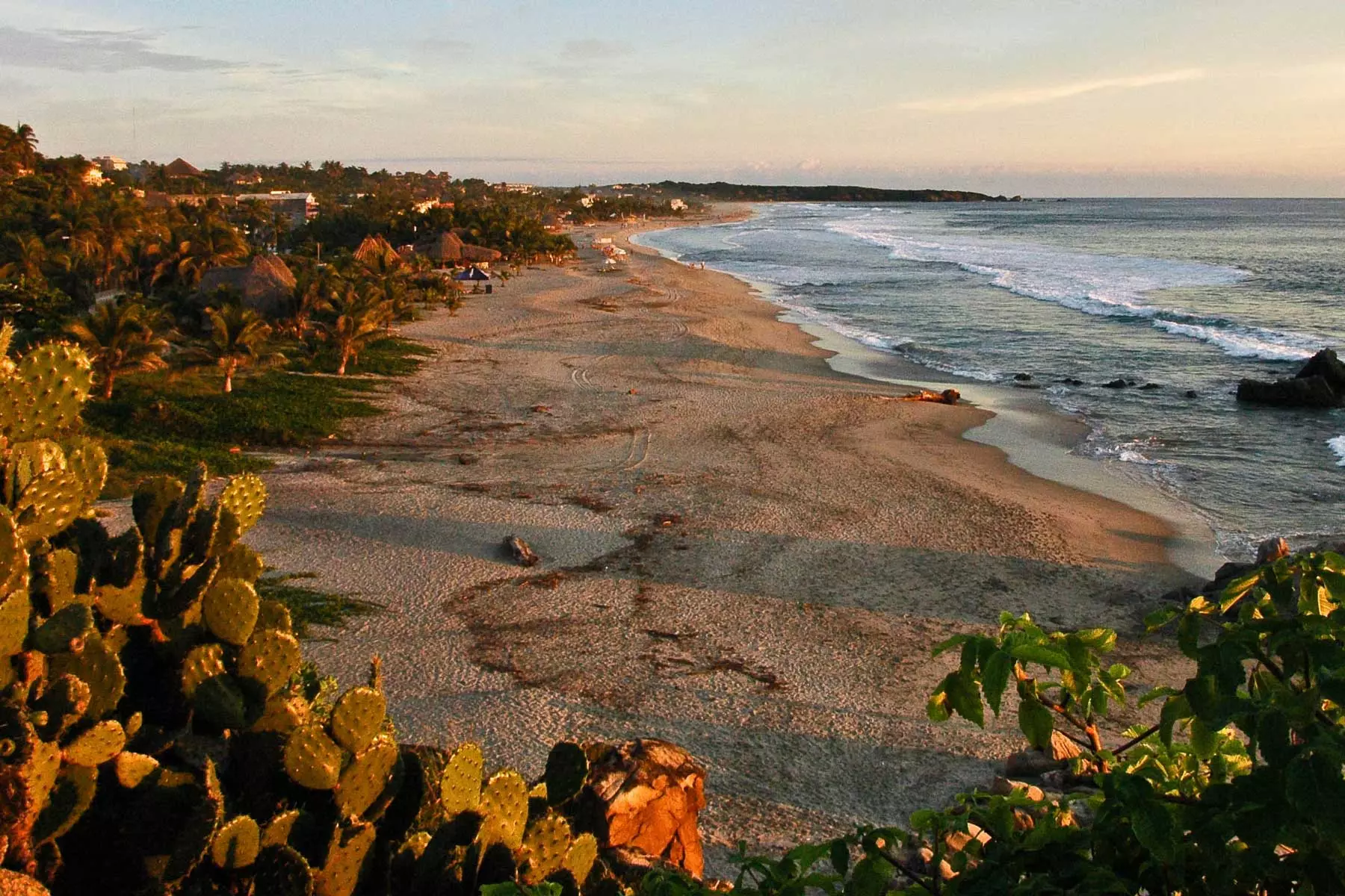 Izuba rirenze hejuru ya Playa Zicatela itagira ubutayu, mugihe imiraba ivuye mu nyanja ya pasifika ije kugwa muri Porto Escondido, Oaxaca, Mexico