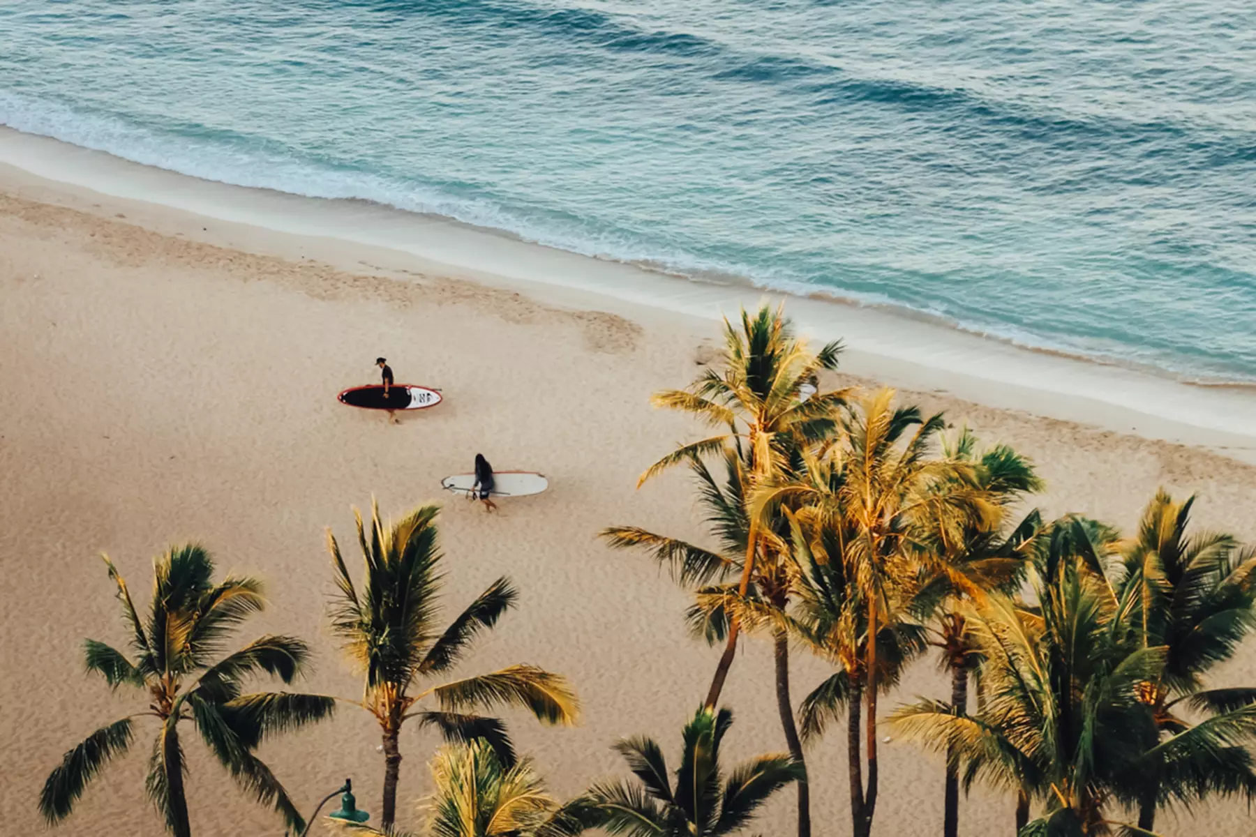 Menschen, die mit Surfbrettern den Strand von Hawaii hinuntergehen