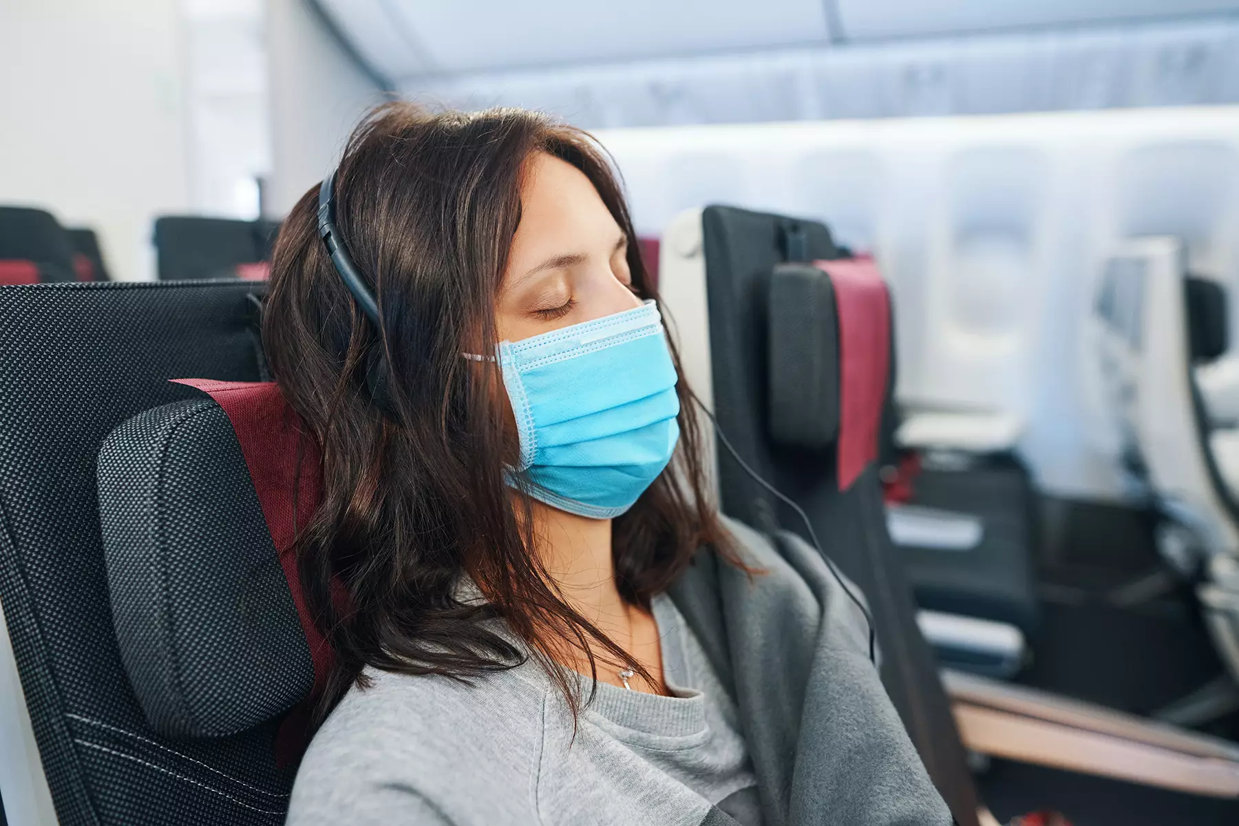 Una donna con una maschera facciale che dorme/riposa su un aereo