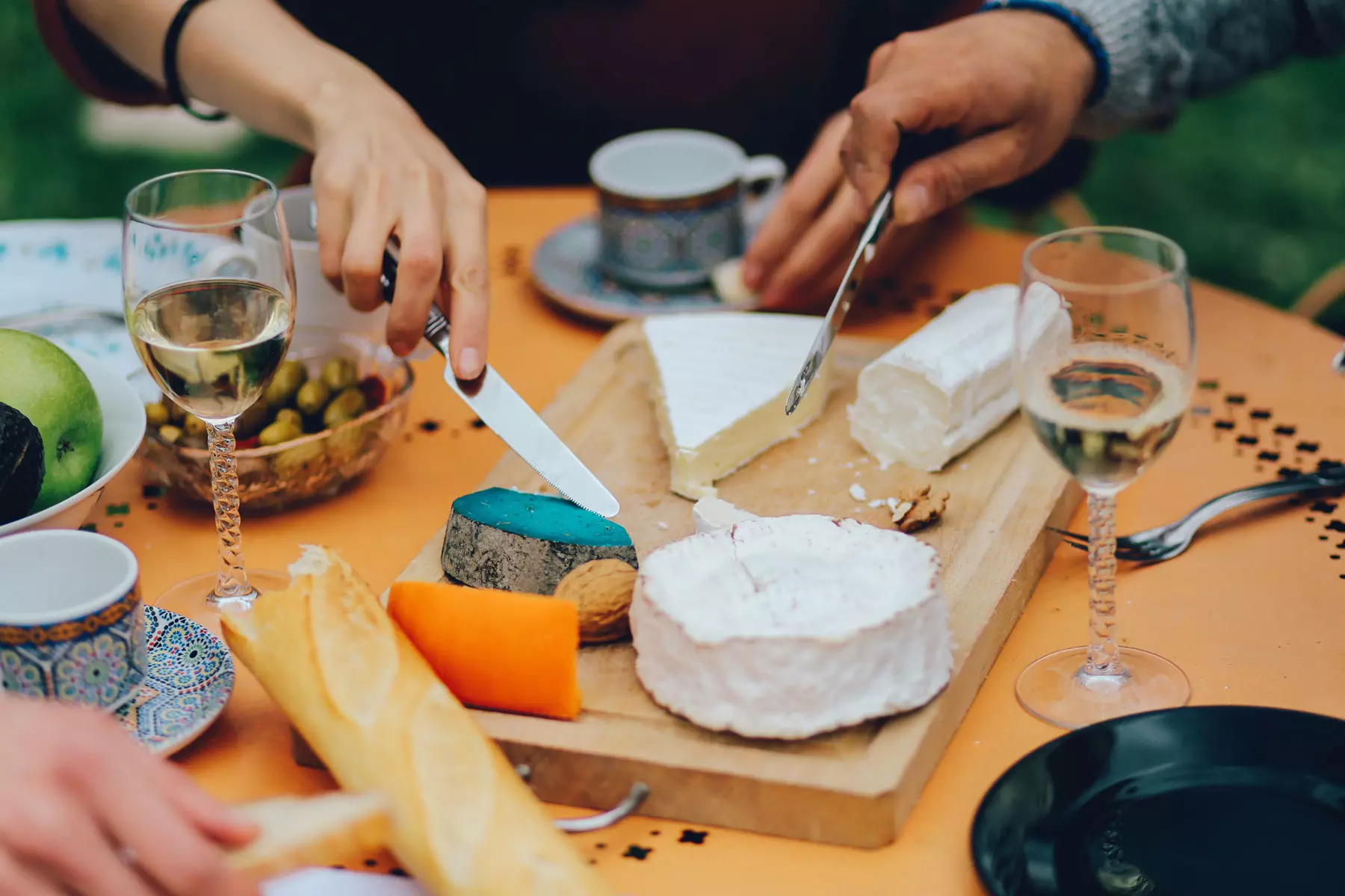 Parisko auzoko etxe bateko lorategian dagoen mahaiaren irudia hurbileko irudia, Frantziako janari tradizionalez, gazta mota ezberdinez, ardoz, etxeko baguette ogiz eta frutaz eta barazkiak beteta.