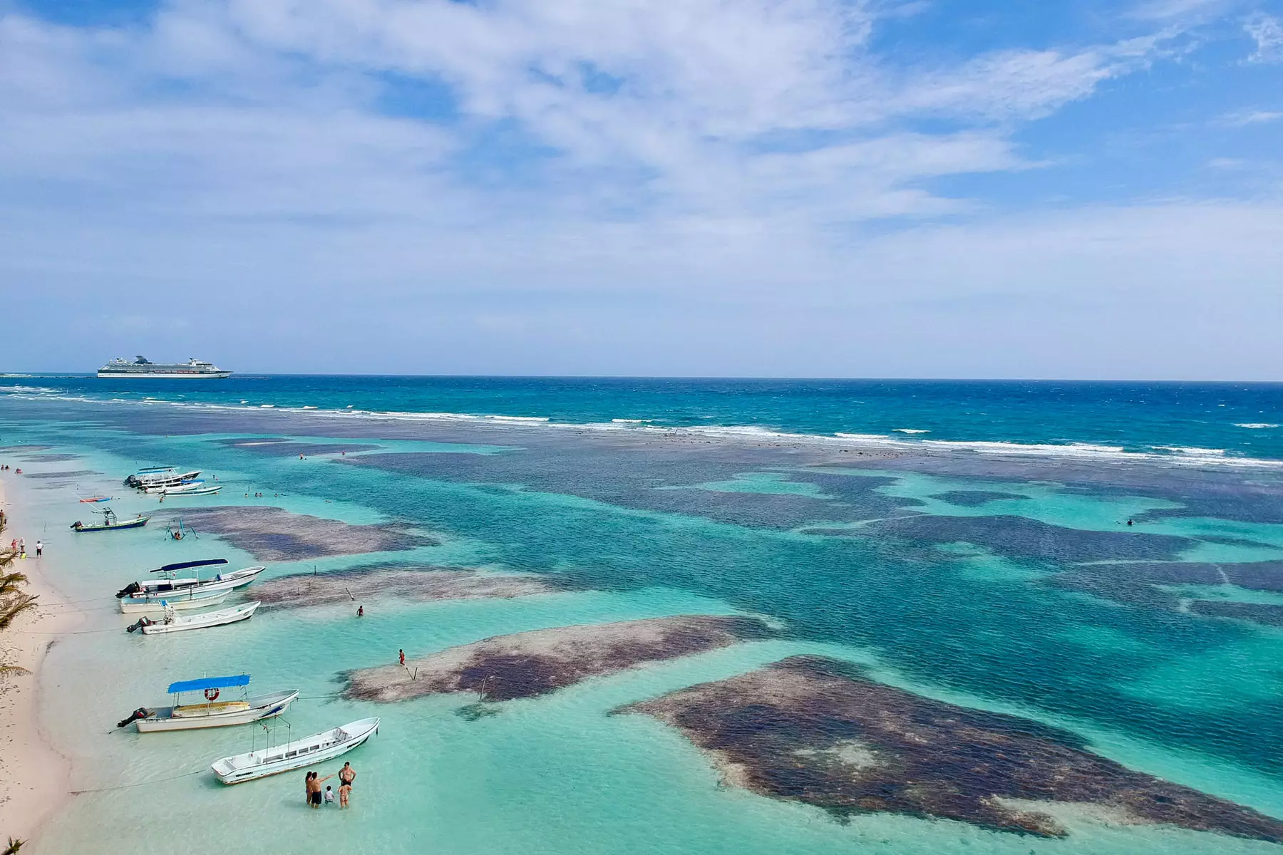 Garis pantai pantai dengan bot dan orang ramai serta kapal persiaran di kejauhan di Mahahual, Mexico