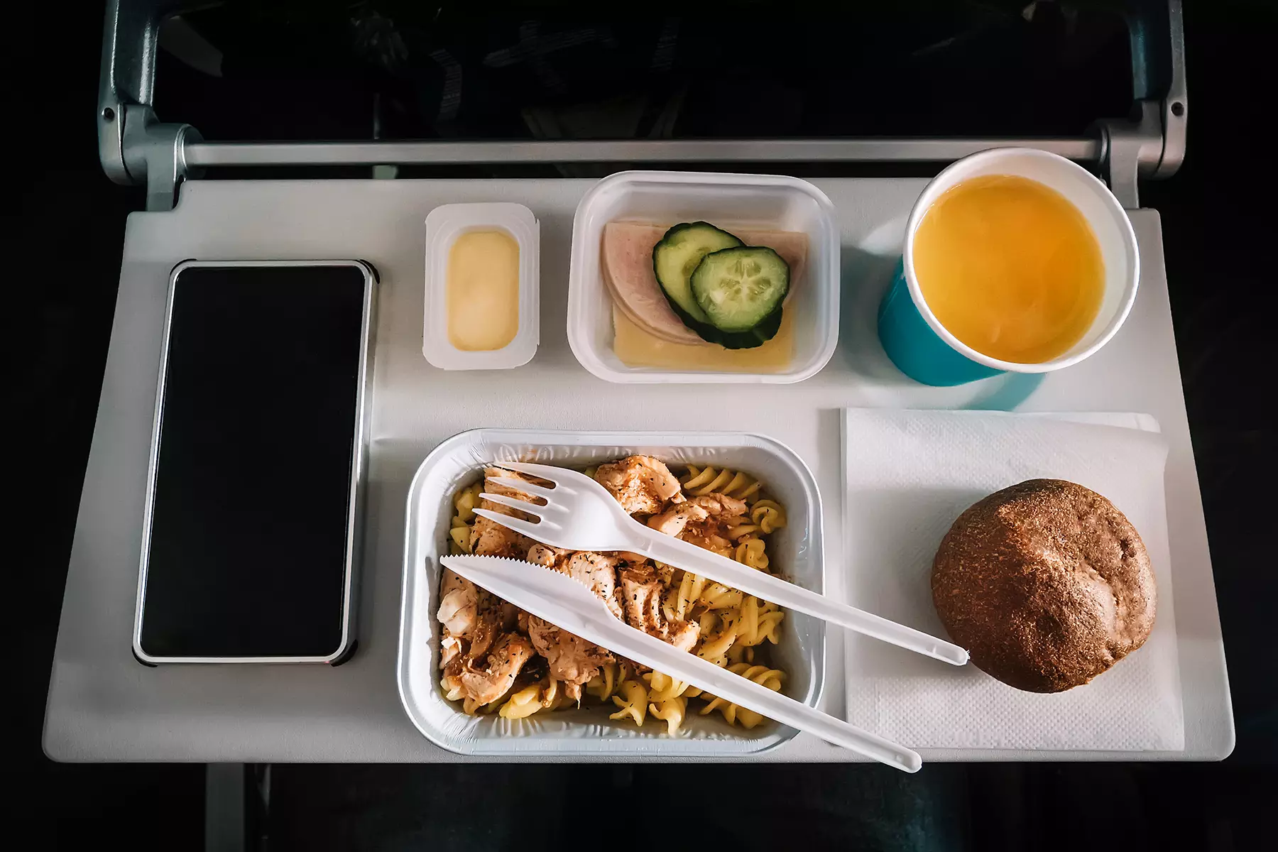 经济舱机上餐盘、肉配意大利面、调味水果、沙拉、黄瓜、一杯果汁和黄油