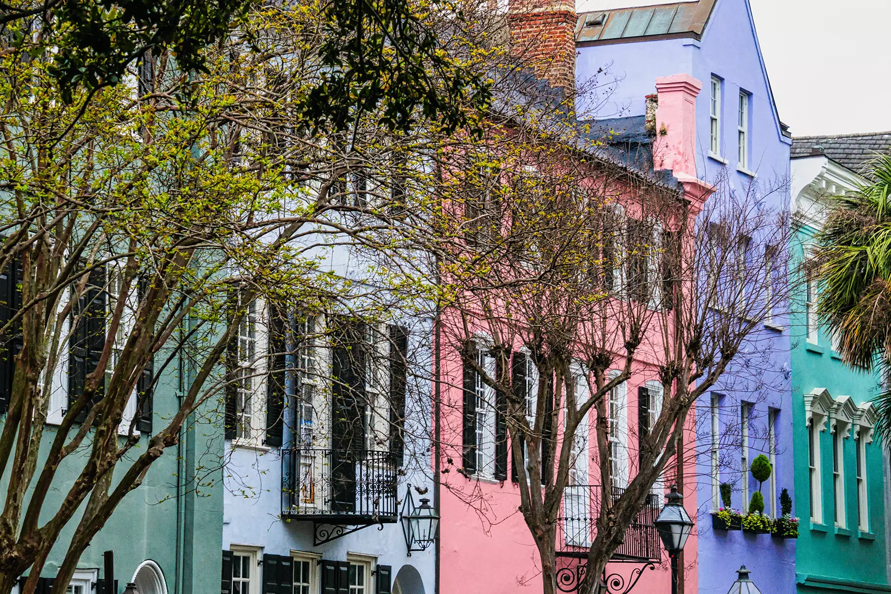 Helder geverfde fasades, gaslanterns en ysterbalkonne versier die fasades van huise langs Charleston se Rainbow Row-distrik.
