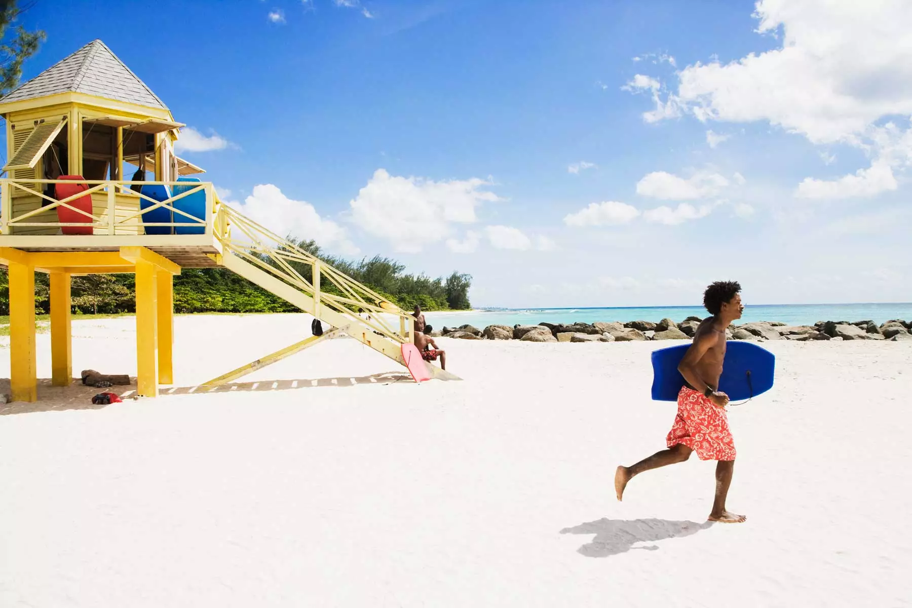 Pria berlari dengan papan tubuh di pantai di Barbados