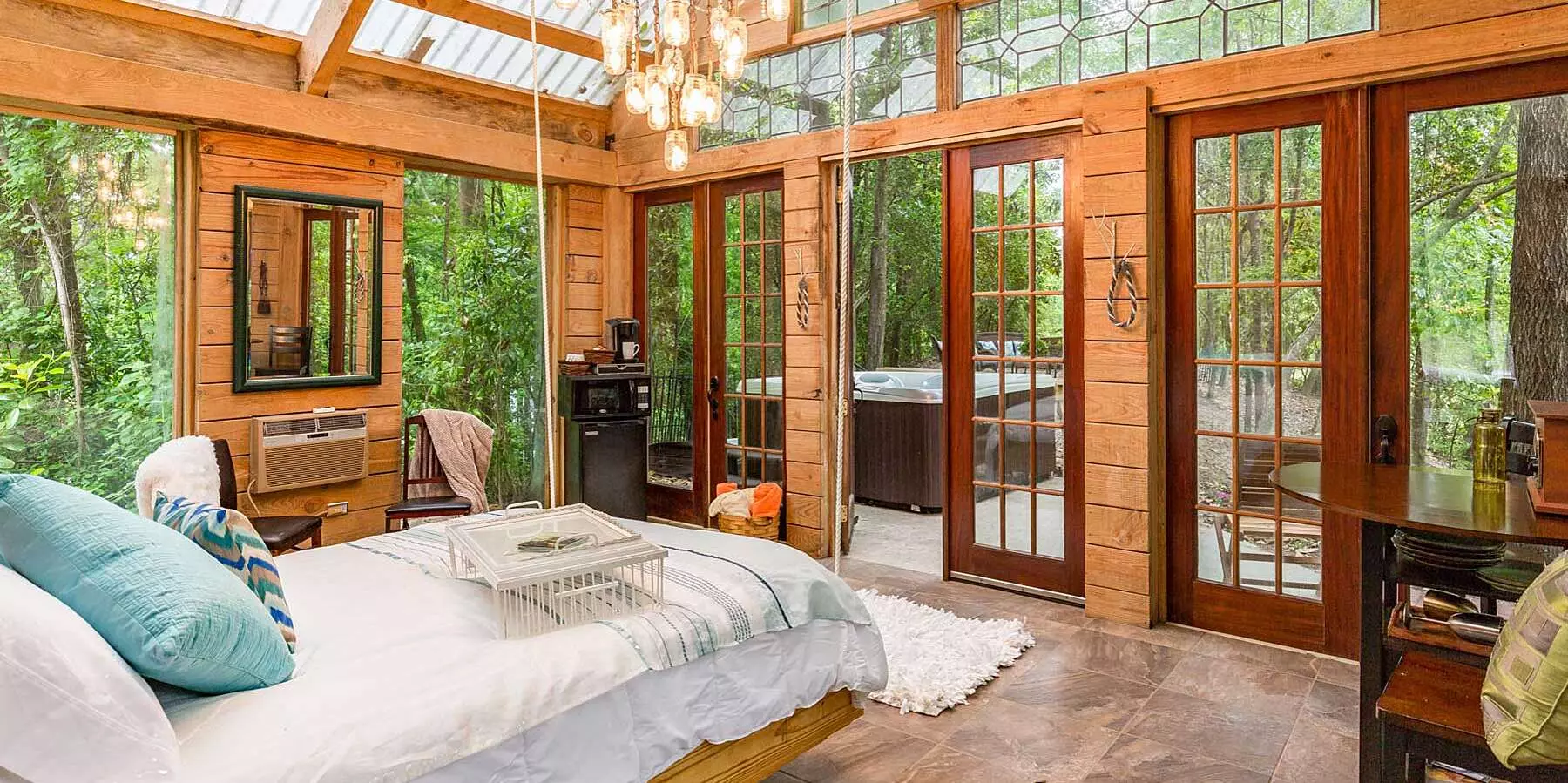 กระท่อมไม้ซีดาร์ในเท็กซัสนี้มีหน้าต่างกระจกสีสวยงาม เตียงแกว่งได้ และอ่างน้ำร้อนกลางป่า