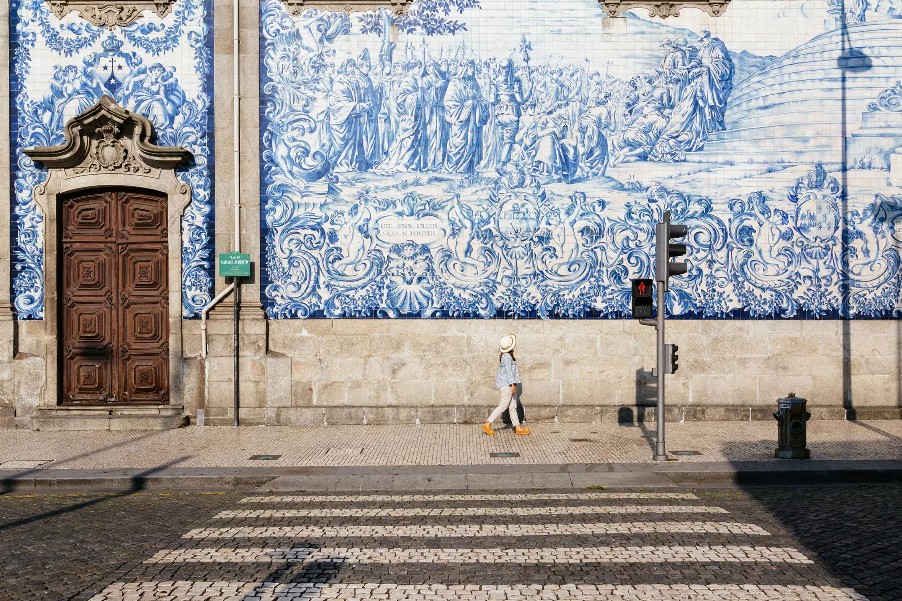 Toeristemeisie loop deur die strate in Porto, teen die azulejos-muur van die Igreja do Carmo-kerk in die agtergrond. Portugal, Europa